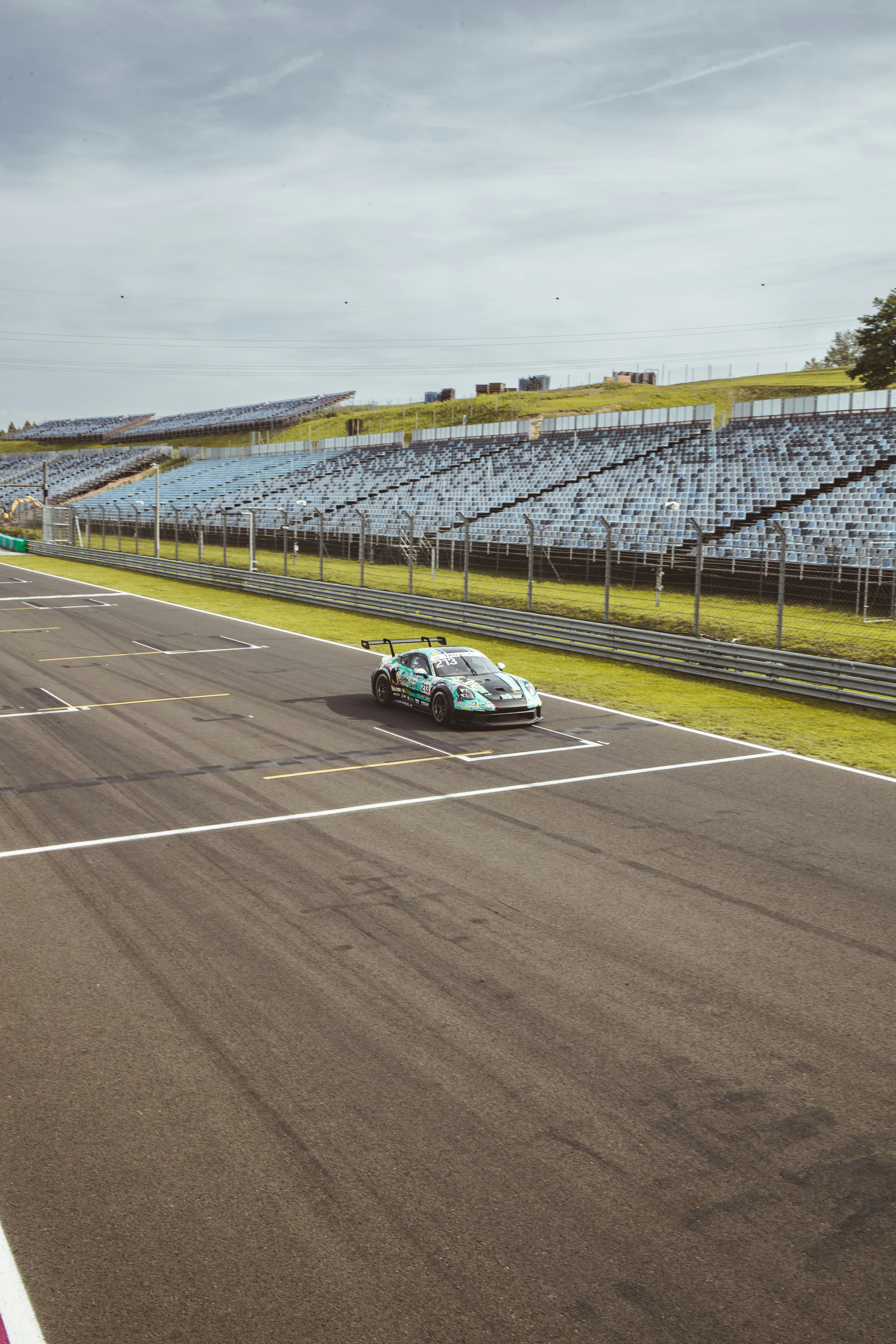 Race car navigating the starting grid at a motorsport venue, surrounded by empty grandstands.