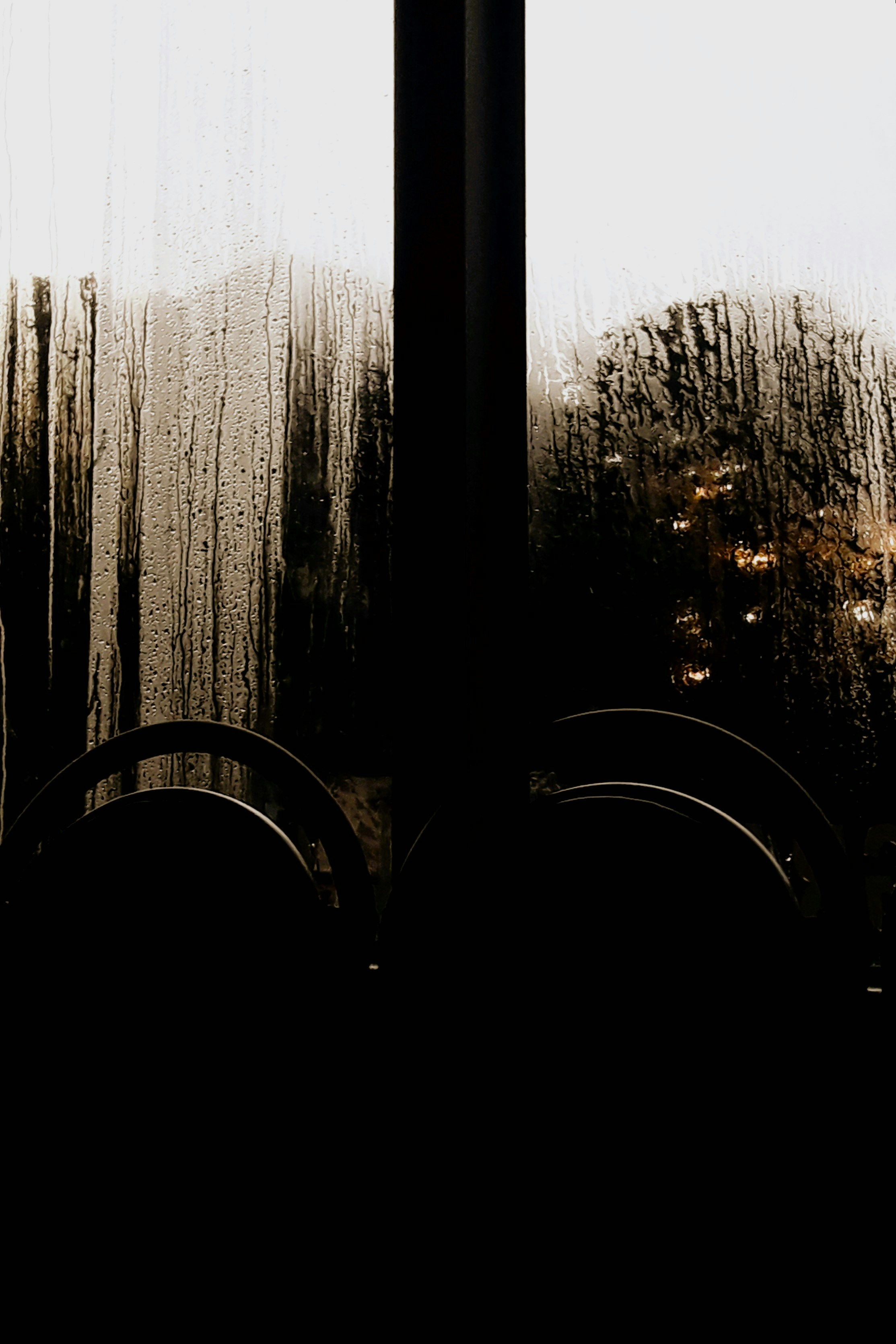 Moody photograph of a rain-streaked window with silhouettes of circular bus seats in the foreground. Distant city lights glow beyond the glass, hinting at the evening outside.