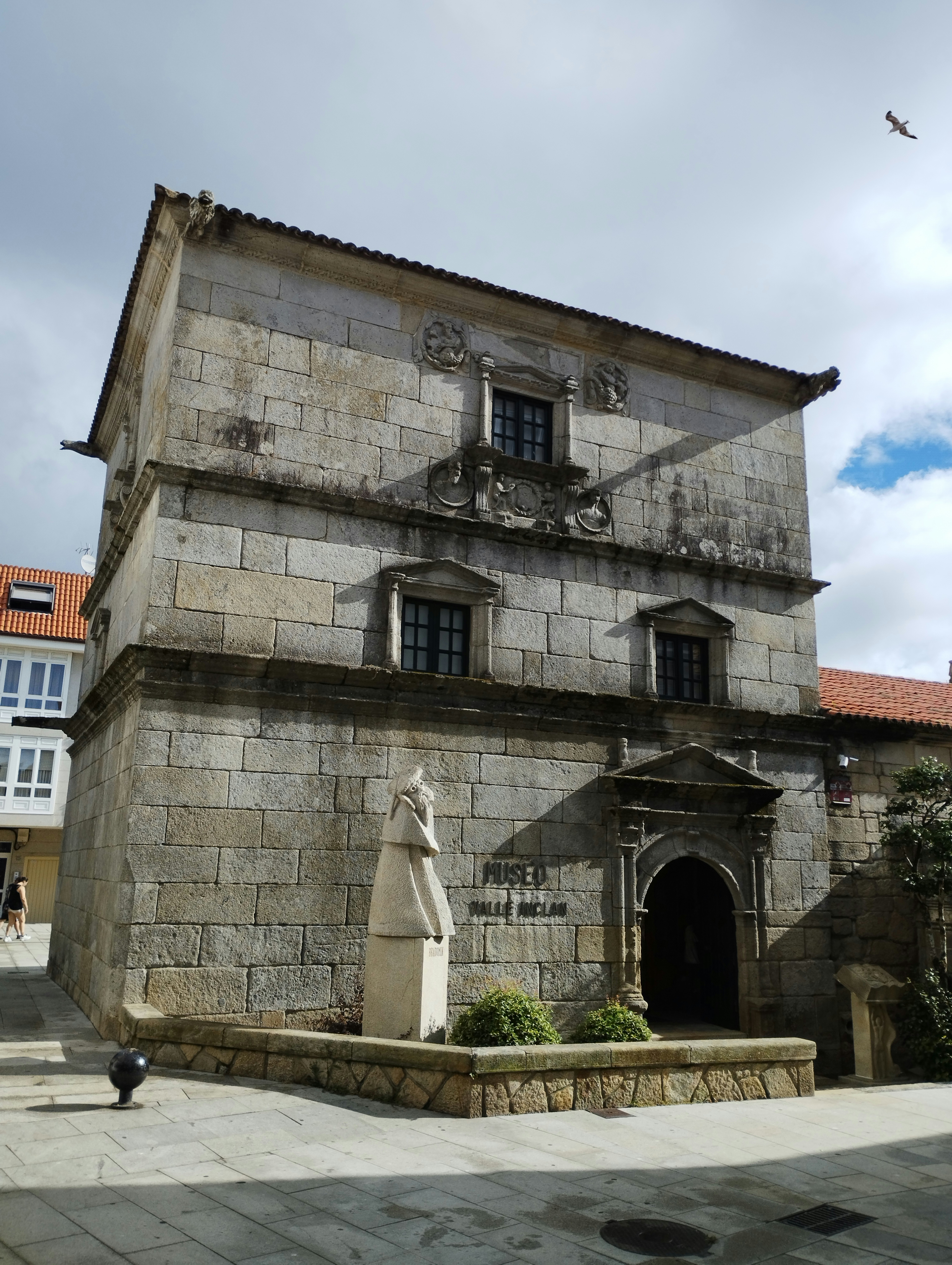 Historic stone museum facade with arched entrance and a statue out front, captured in bright daylight.