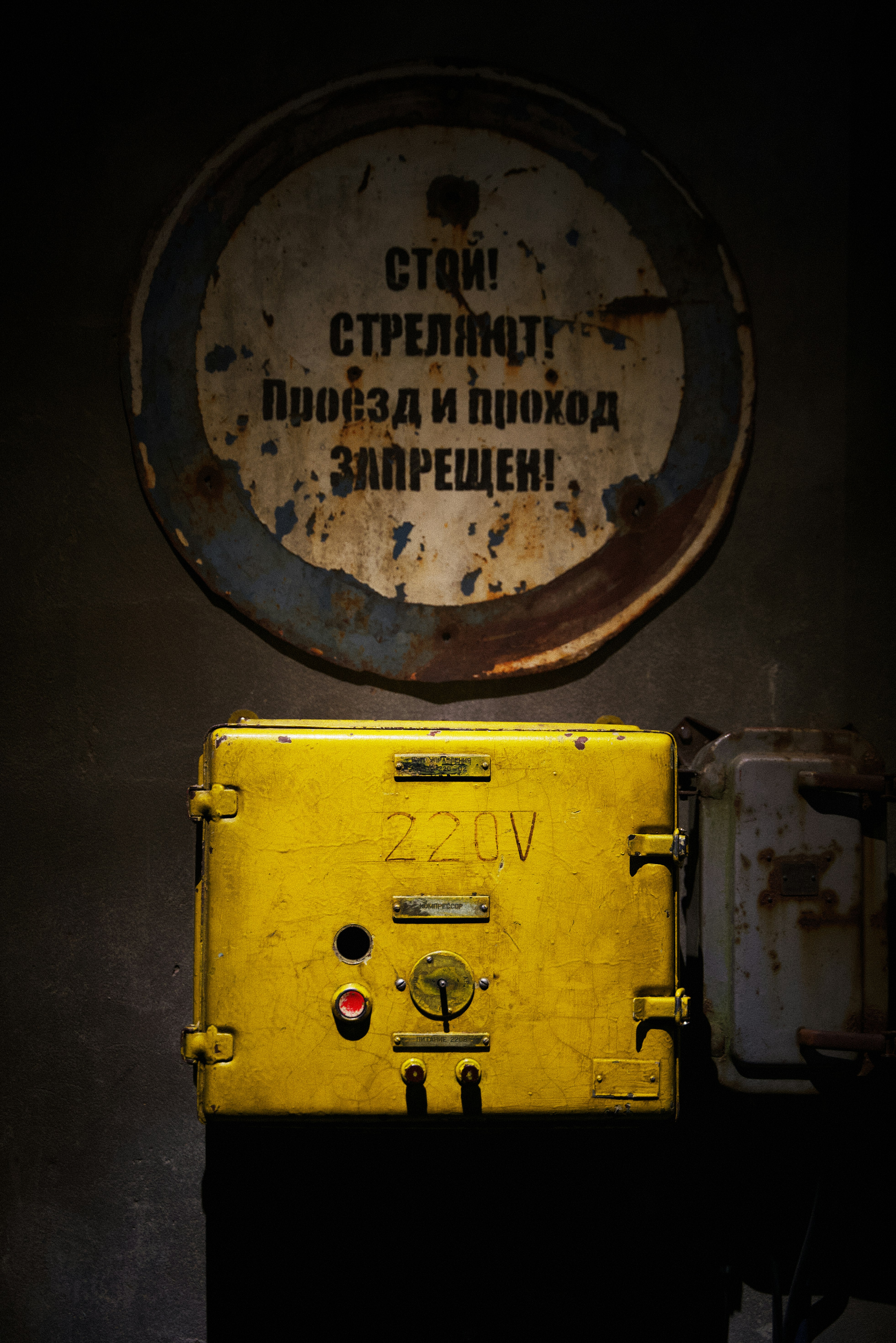 Voltage in Rust: A Weathered Yellow 220V Control Box Under a Circular Warning Sign