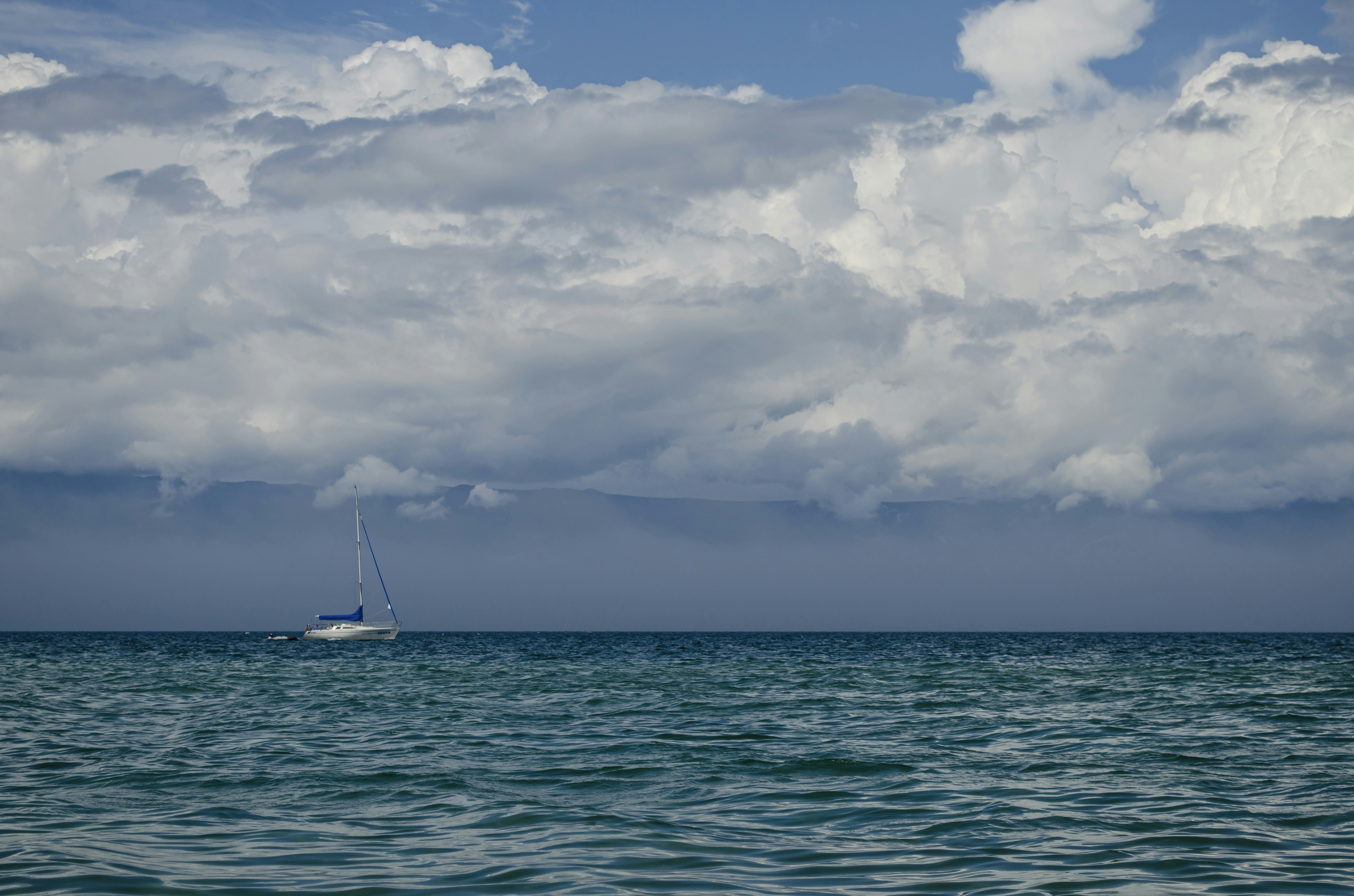 Sailboat drifting on a tranquil sea beneath dramatic, billowing clouds.