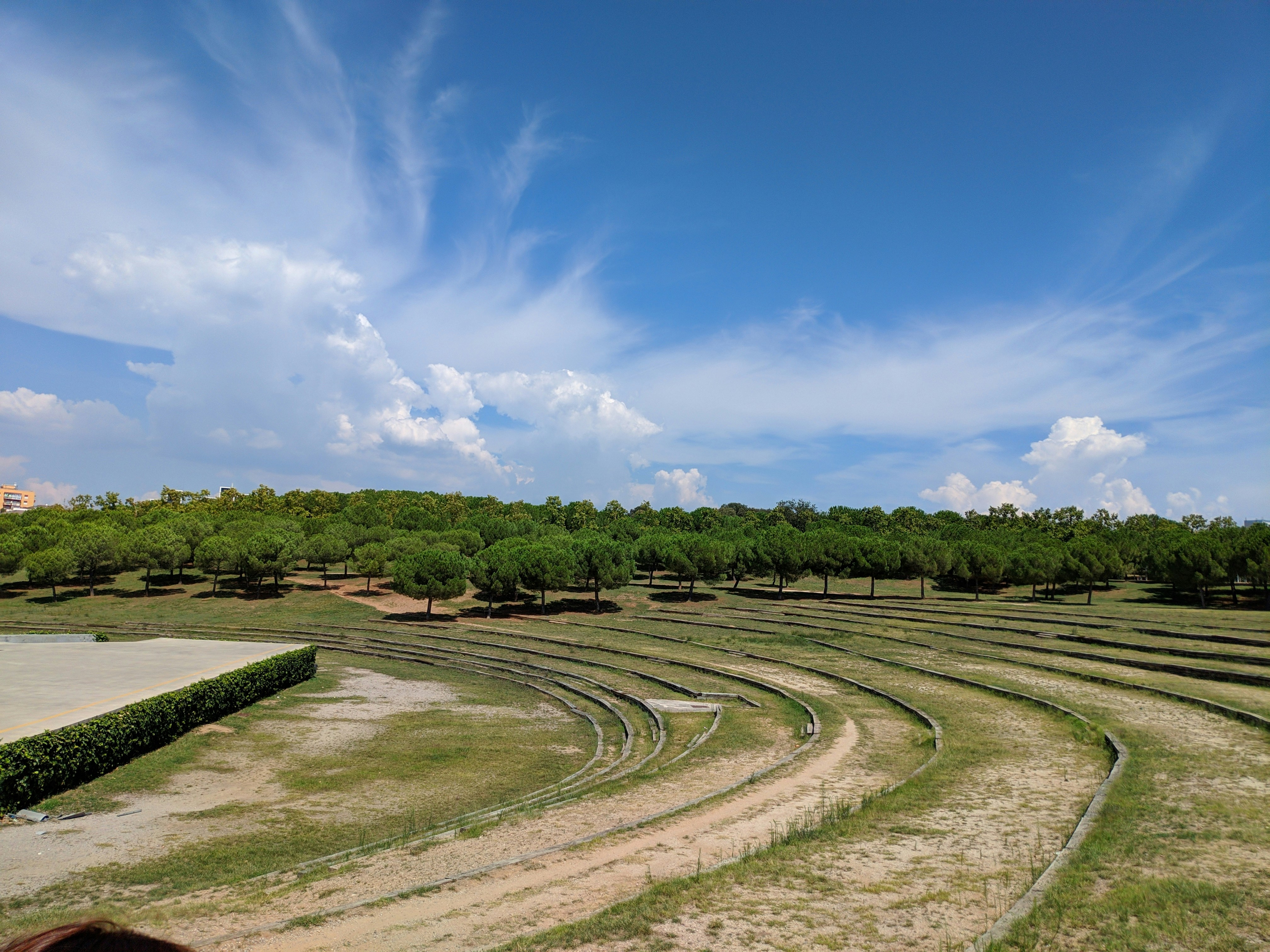 Rolling hills with curved paths under a vibrant blue sky dotted with clouds.