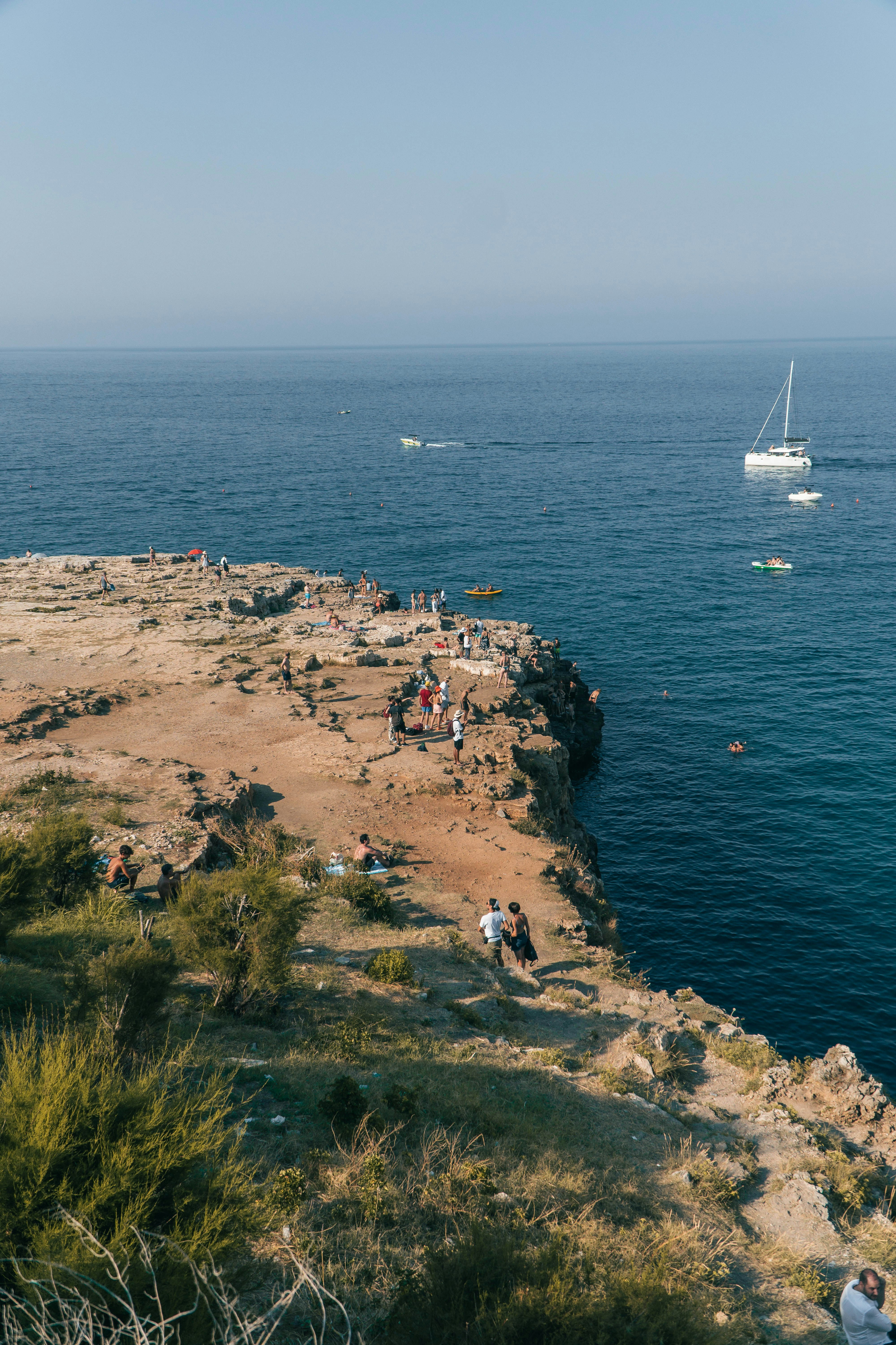 Cliffside Vista: People Gather Along the Coastal Rim as Boats Drift Offshore