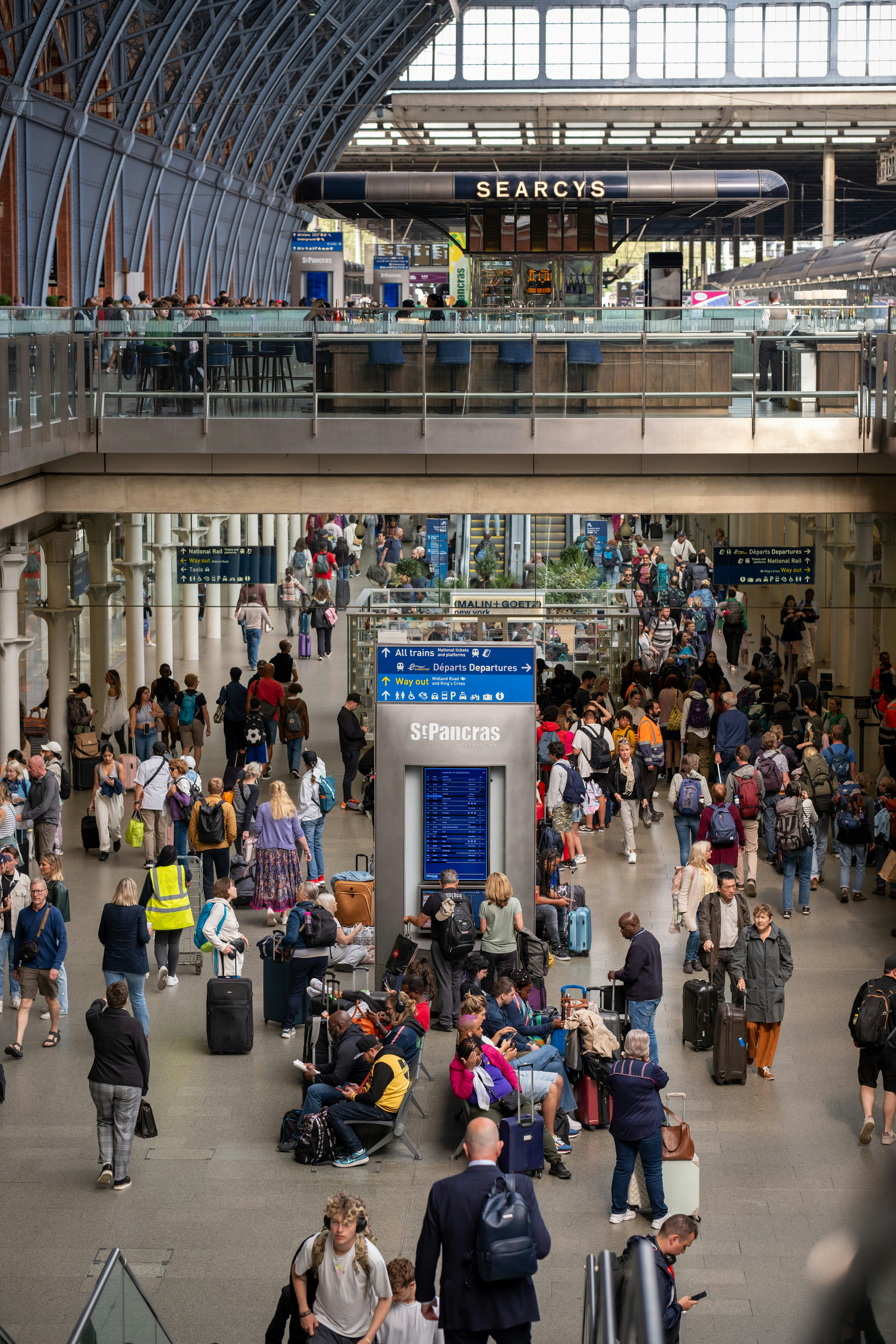 Busy scene at St. Pancras Station, showcasing travelers navigating the terminal with luggage and digital departure boards. The architectural details enhance the bustling atmosphere.