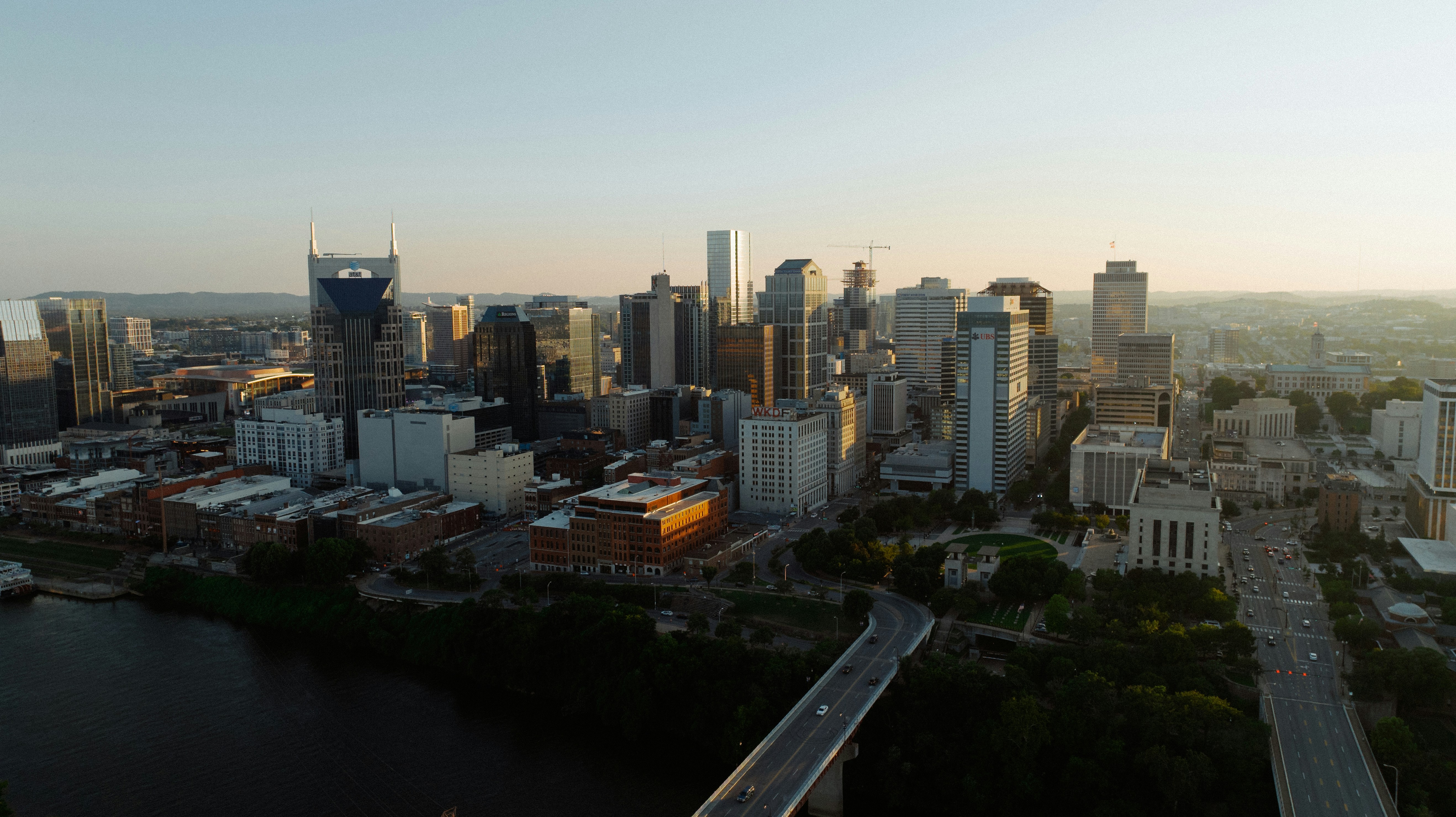 Aerial view of Nashville's skyline showcasing a blend of modern architecture and historical buildings along the river. The scene captures the city's vibrant atmosphere during sunset.