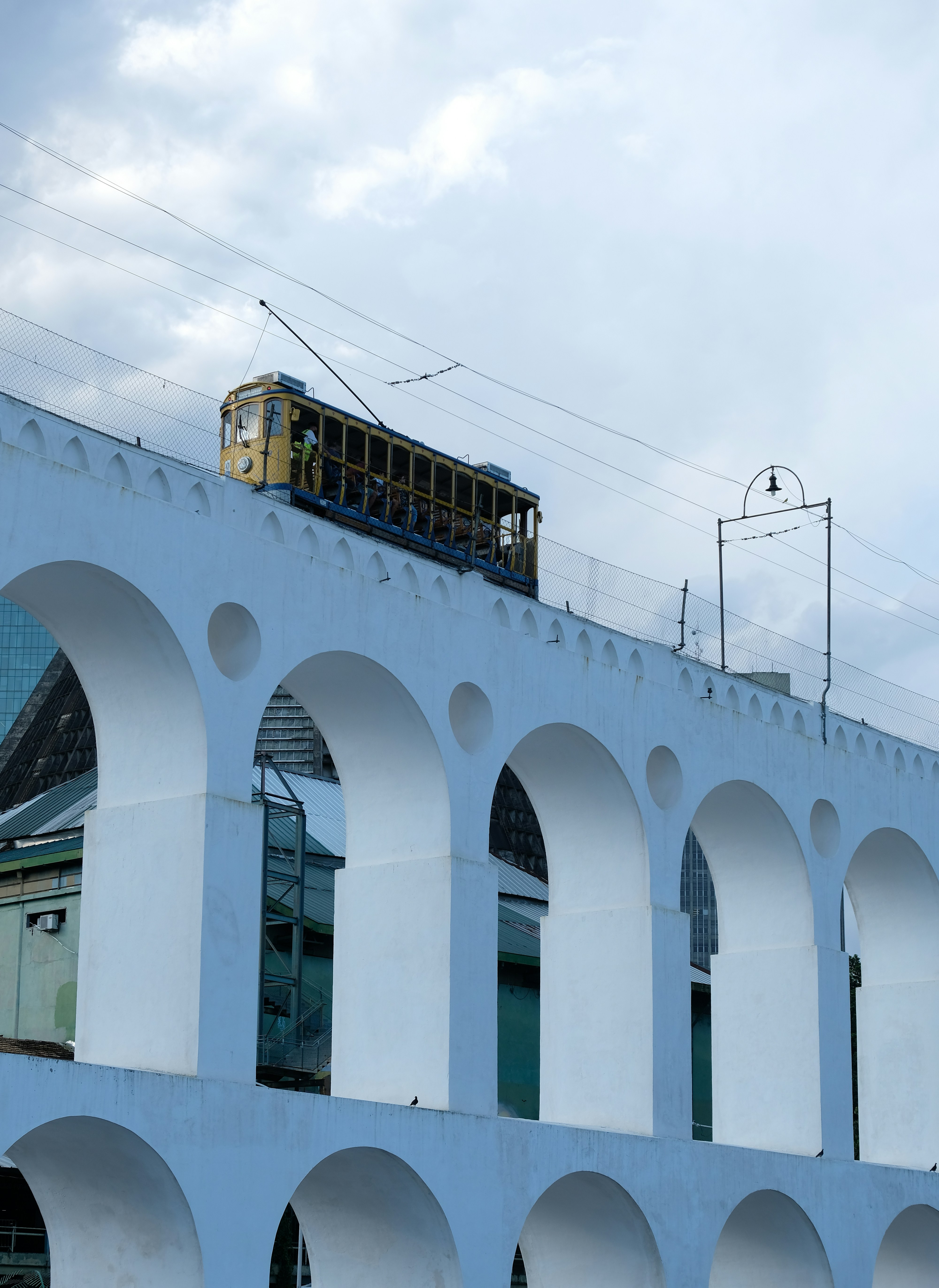 Yellow Tram Crossing a White-Arched Aqueduct Under a Moody Sky