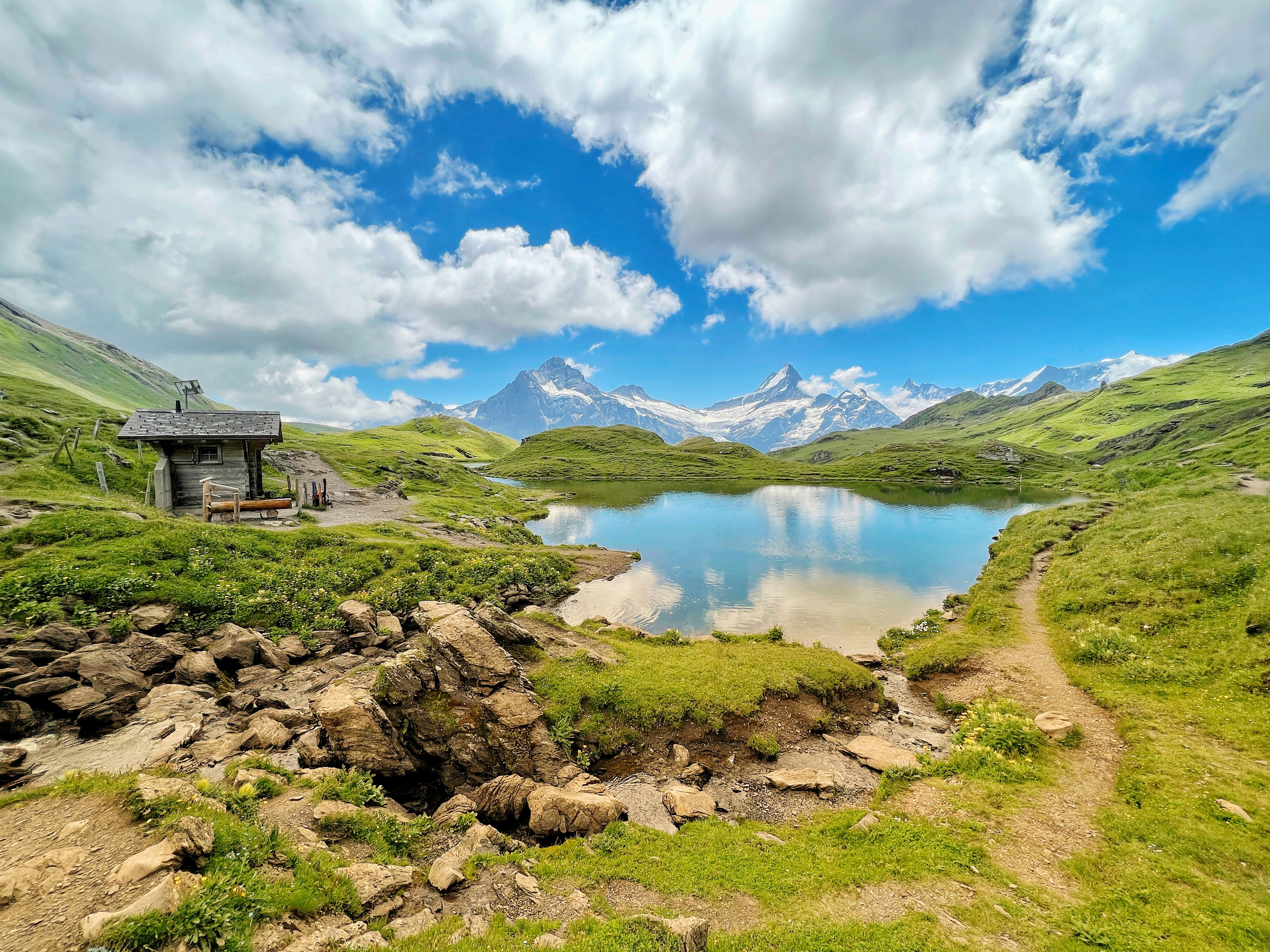 Azure Mirror: Alpine Lake Framed by Green Slopes and Snow-Kissed Peaks