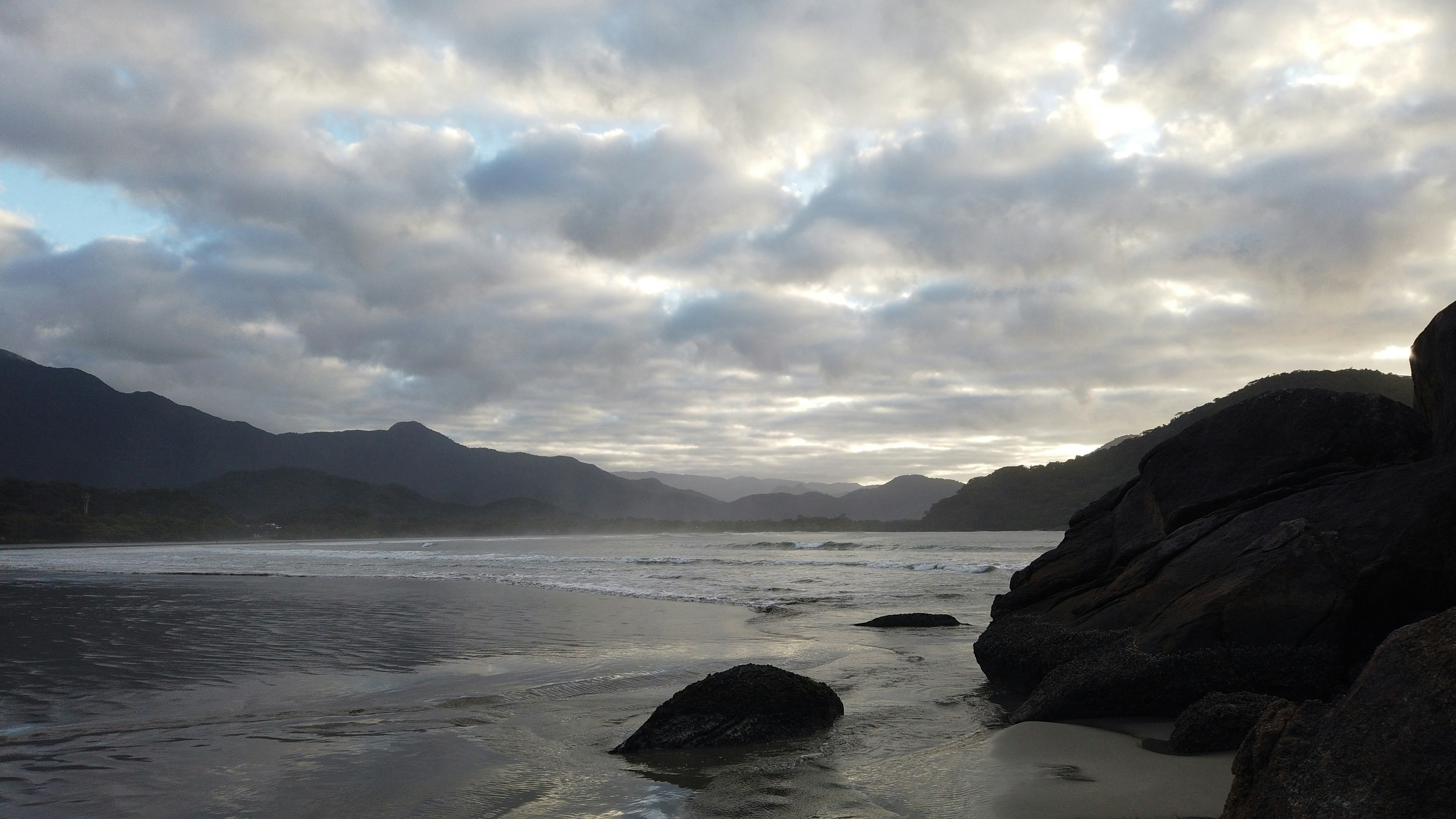 Rocky shoreline meeting calm waters under a cloudy sky at dusk.