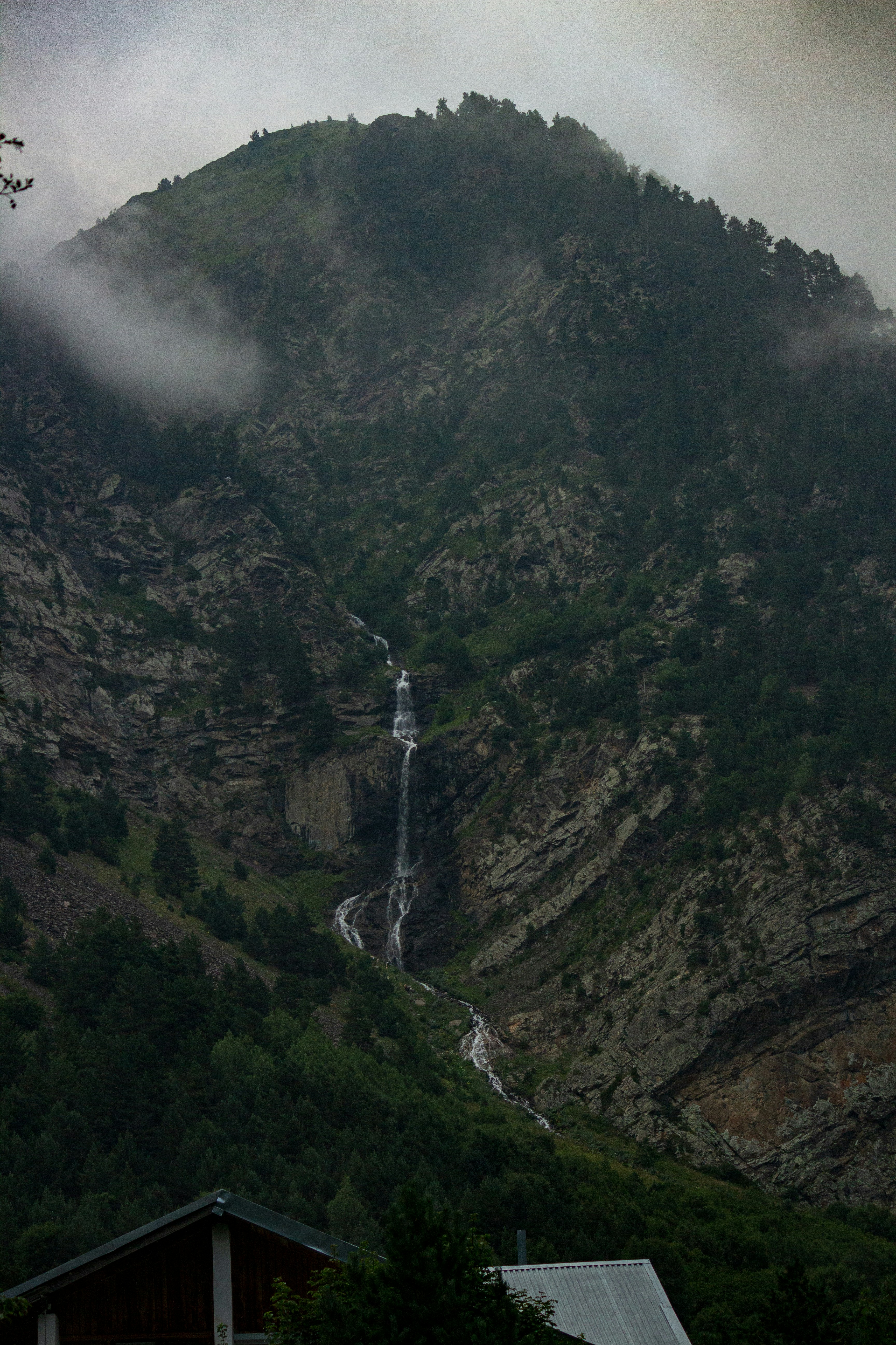 Alpine Cascade Winding Down a Craggy Ridge Beneath Veiling Mist