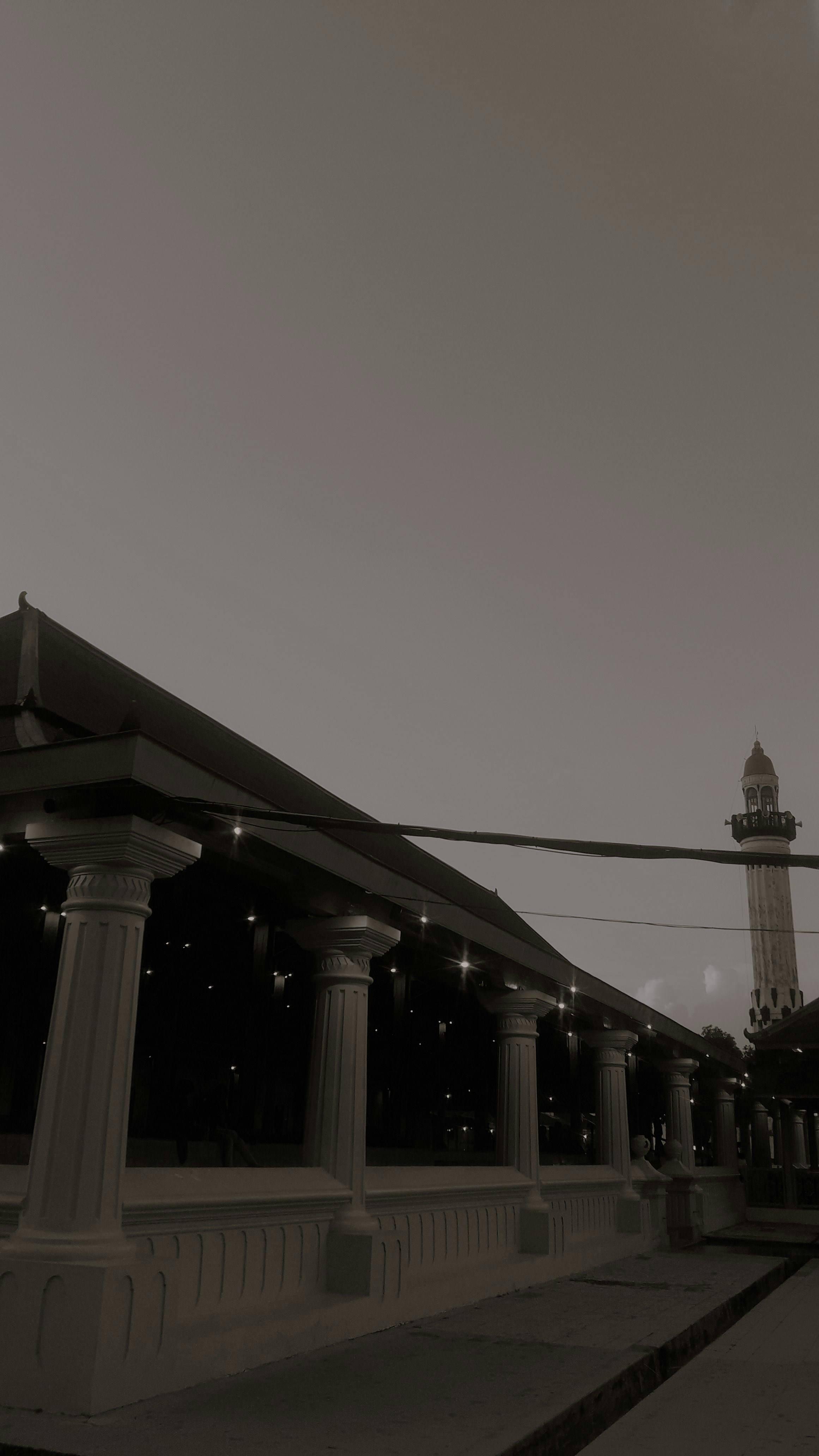 Dusky photograph of a colonnade with classical columns and string lights, guiding the eye toward a distant minaret against a pale sky.
