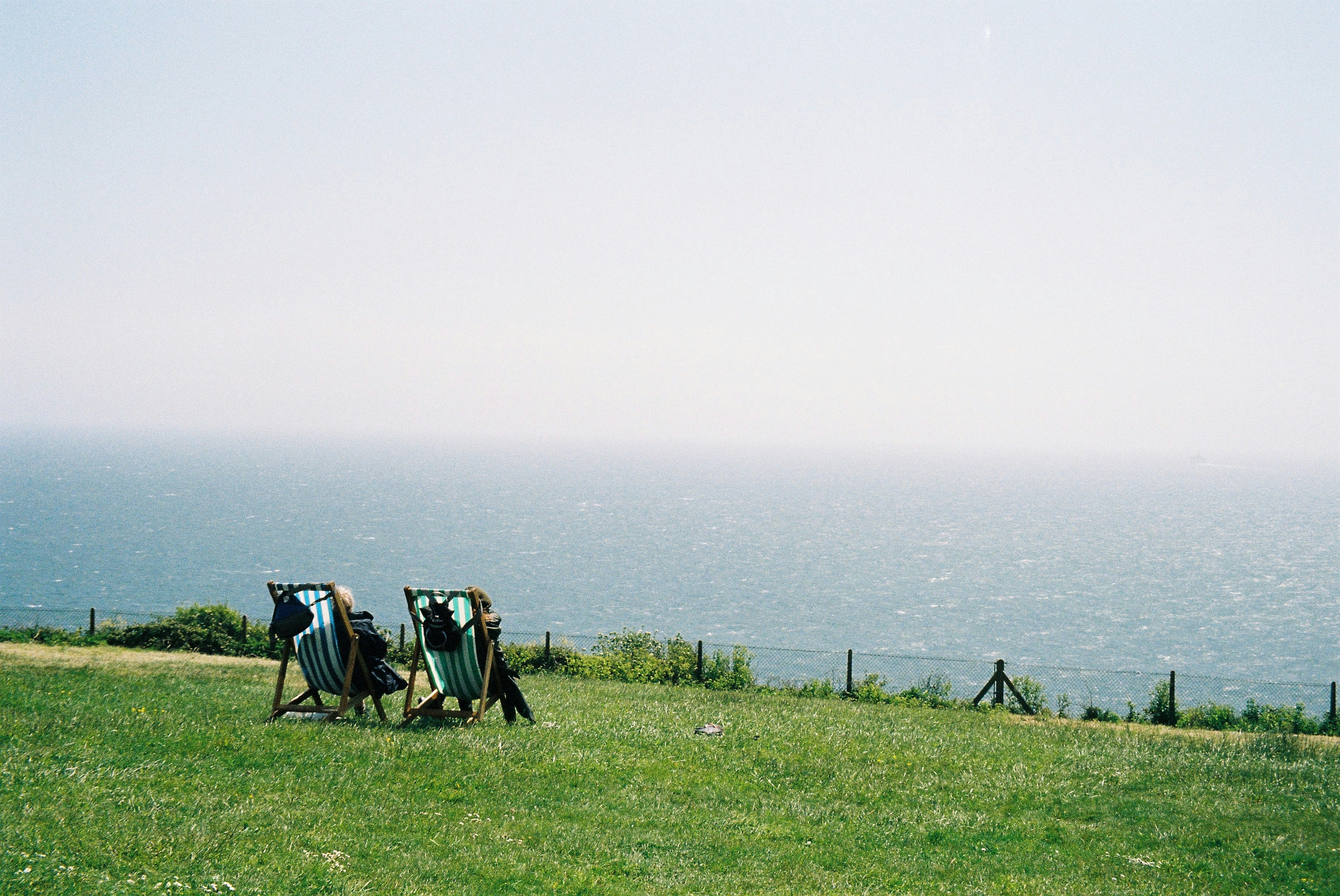 Two Deck Chairs on a Grassy Cliff, Watching the Sea