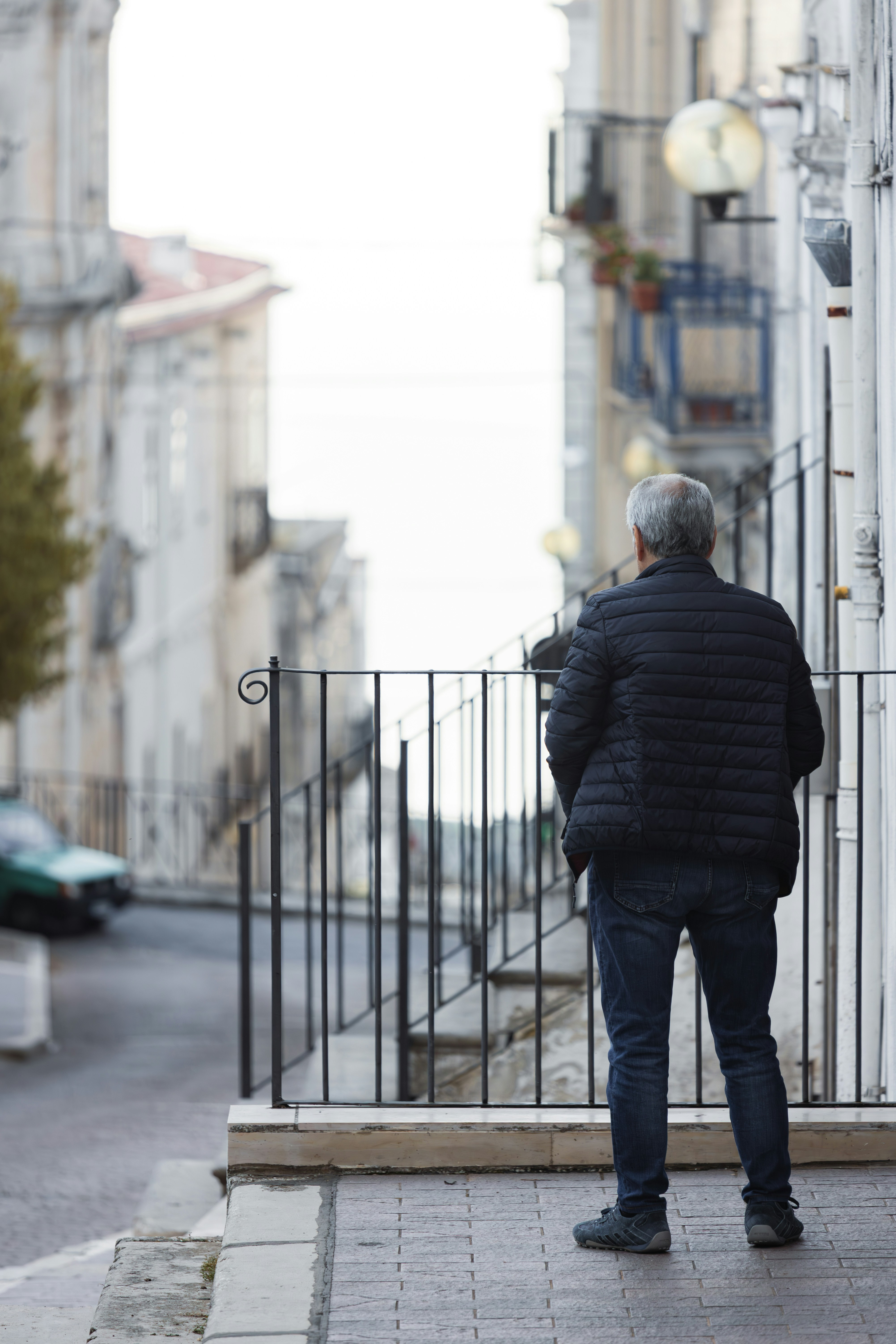 Man in a dark jacket stands on a cobblestone street, gazing at an empty road lined with historic buildings.