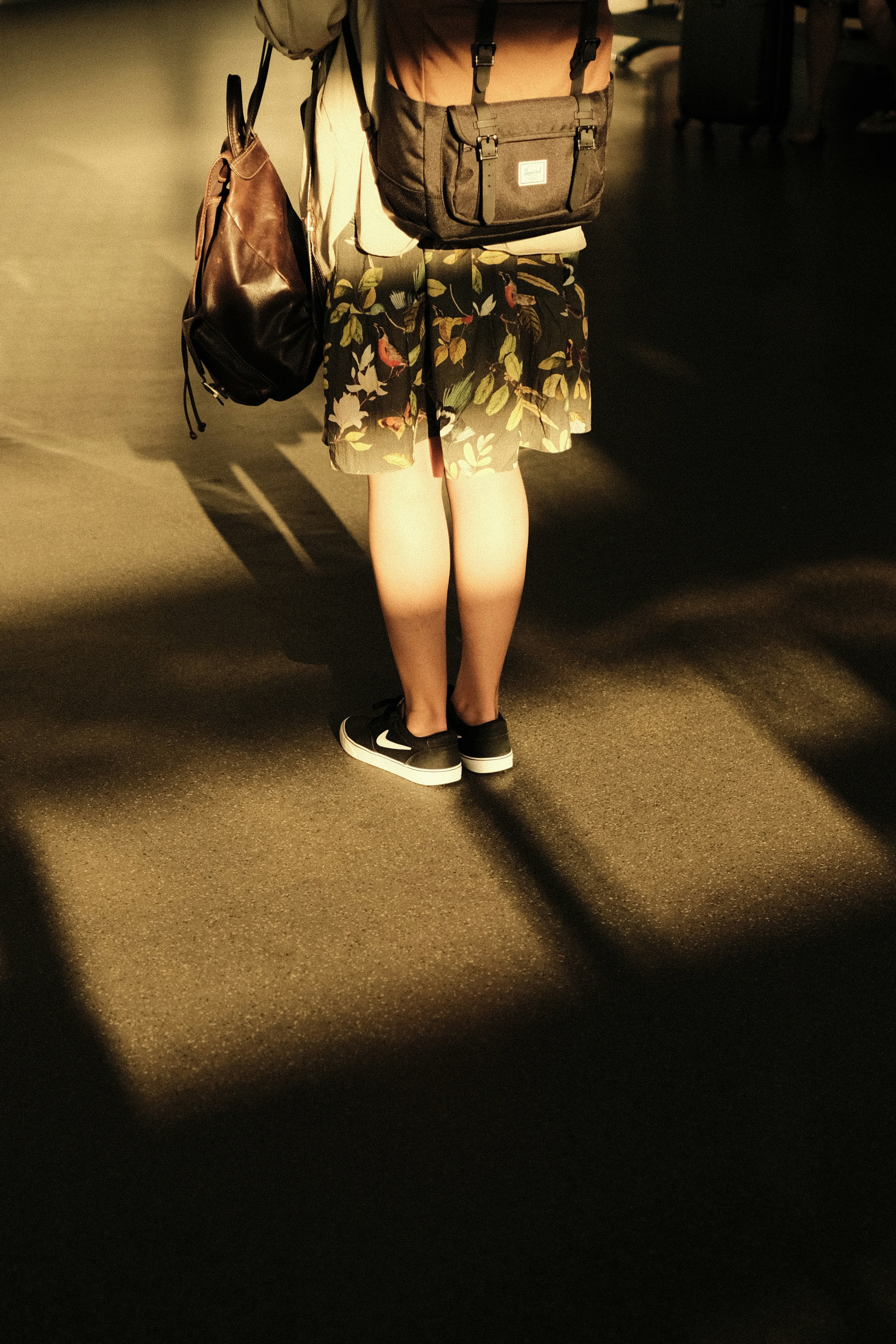 Amber Walk: Floral Skirt, Backpack, and Sneakers in a Shadowed Gallery