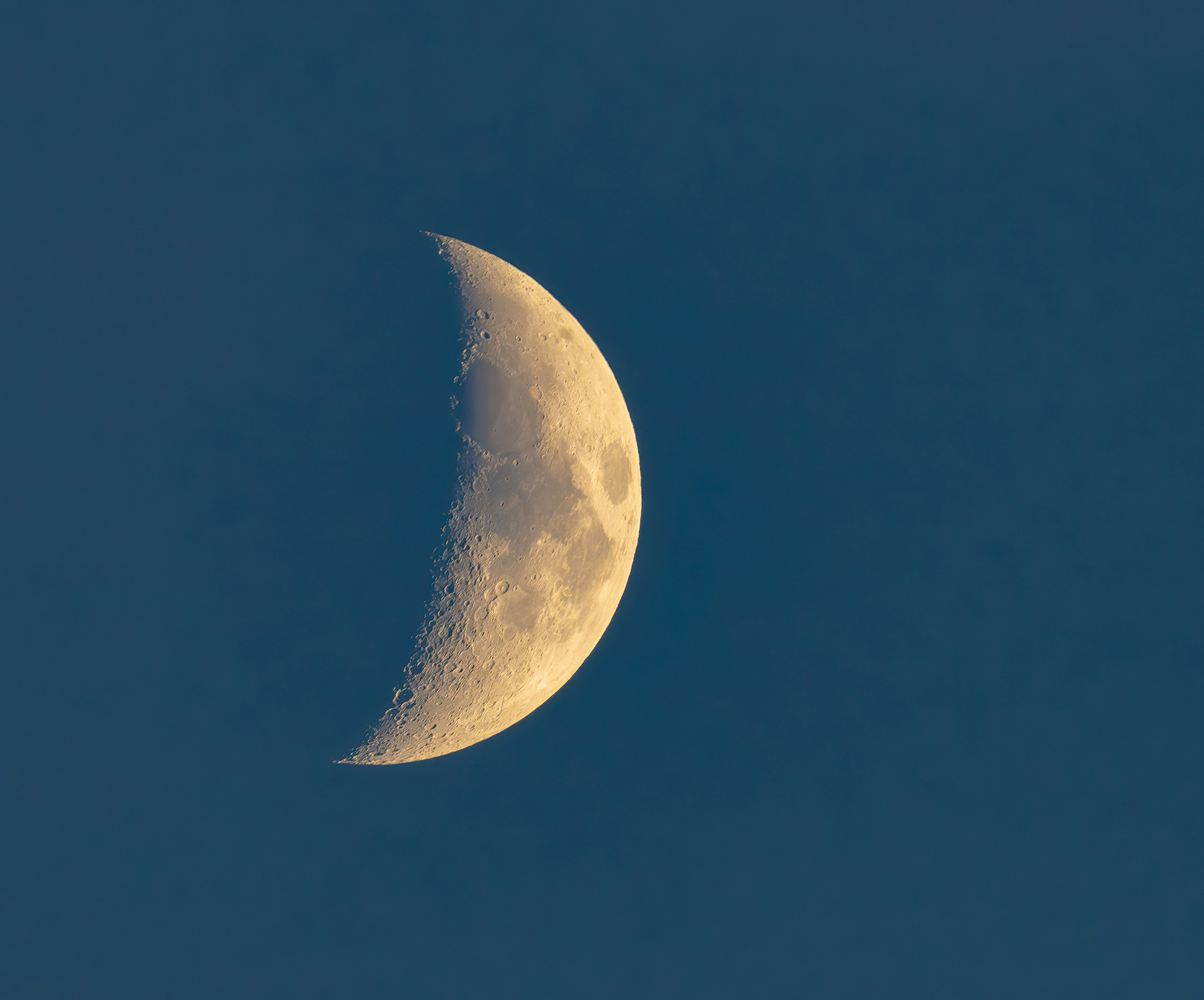 Waxing crescent moon illuminated against a deep blue sky, showcasing its craters and textures.