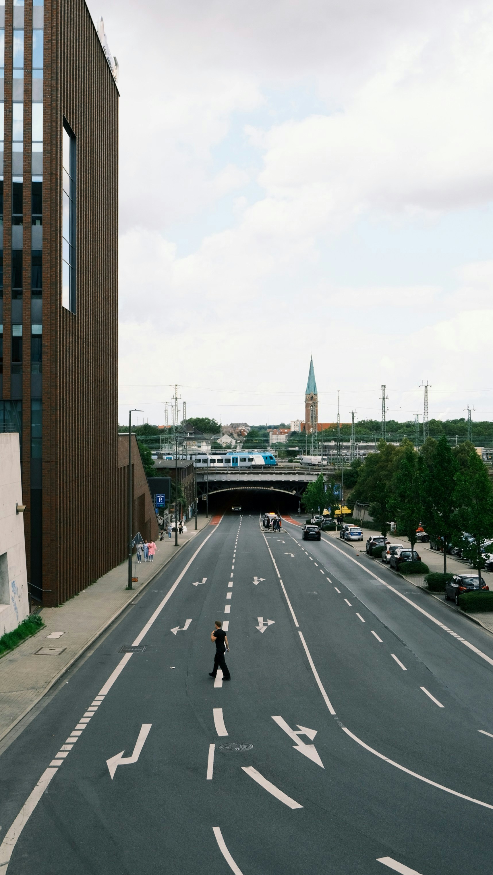 Crossing the City Artery: A solitary figure toward a distant spire