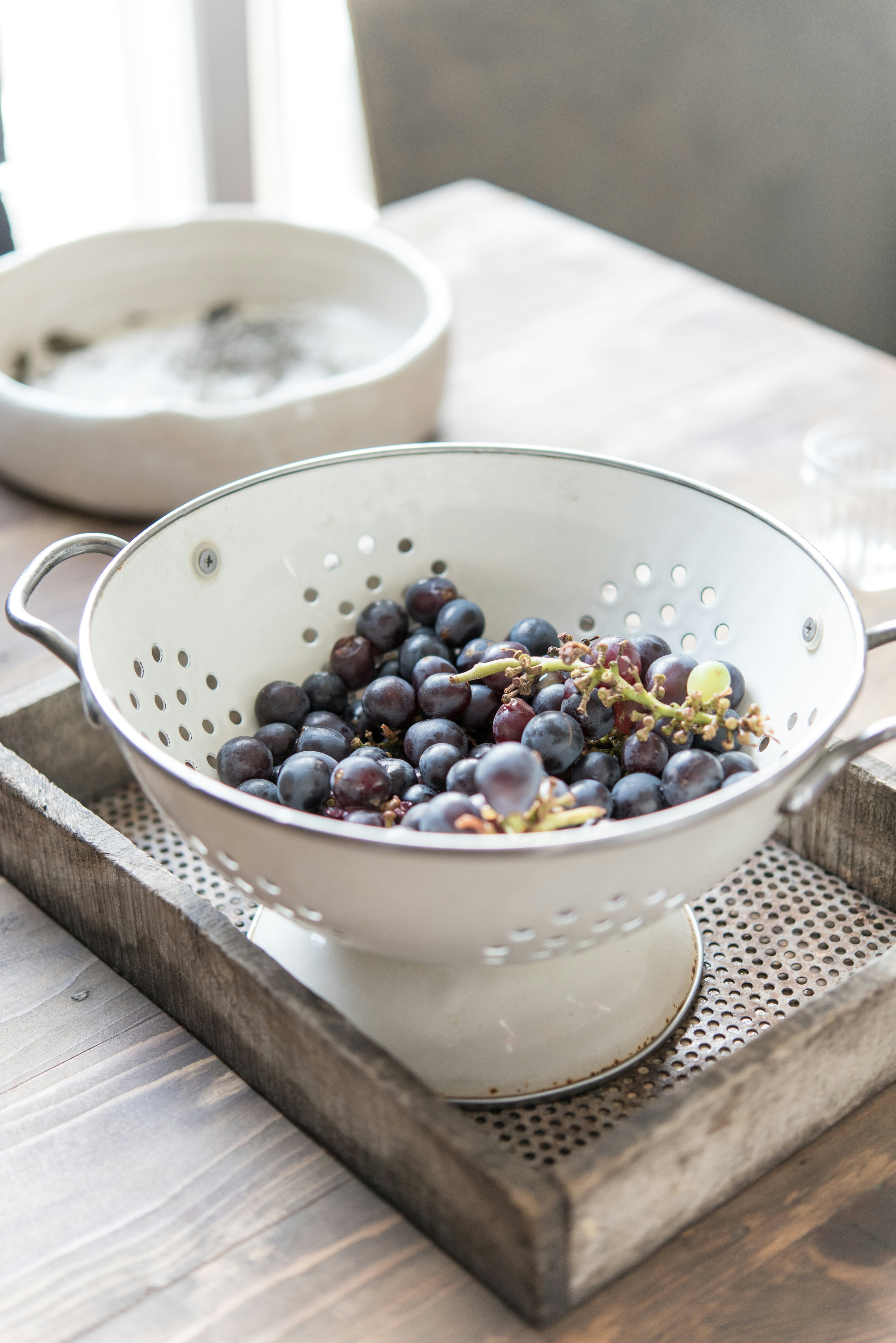 A white colander filled with grapes on top of a wooden tray photo ...