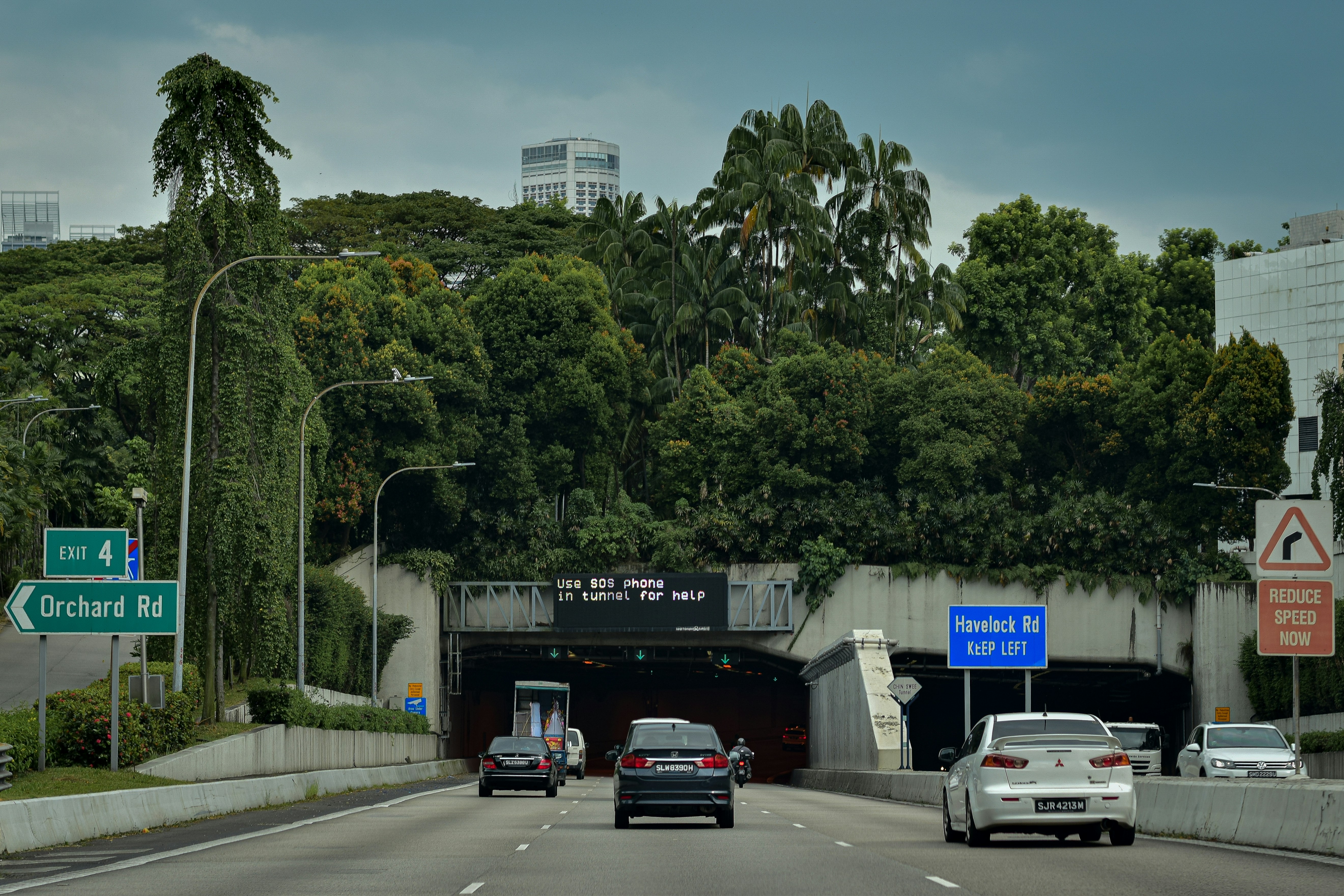 Cars navigating a highway entrance beneath a vibrant green canopy, with directional signs guiding the way.