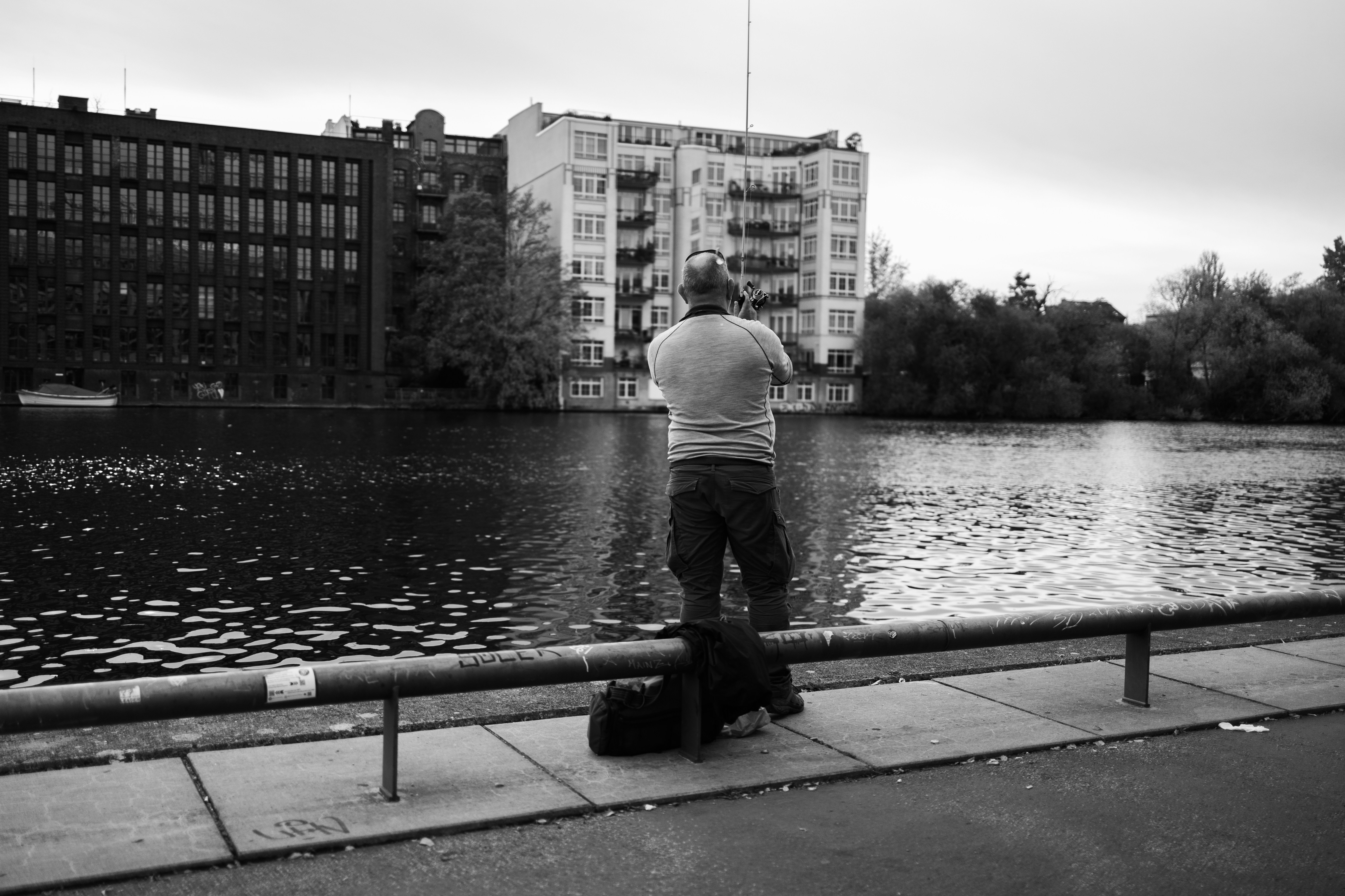 Riverside Gazer: A Lone Photographer Framed by Water and City