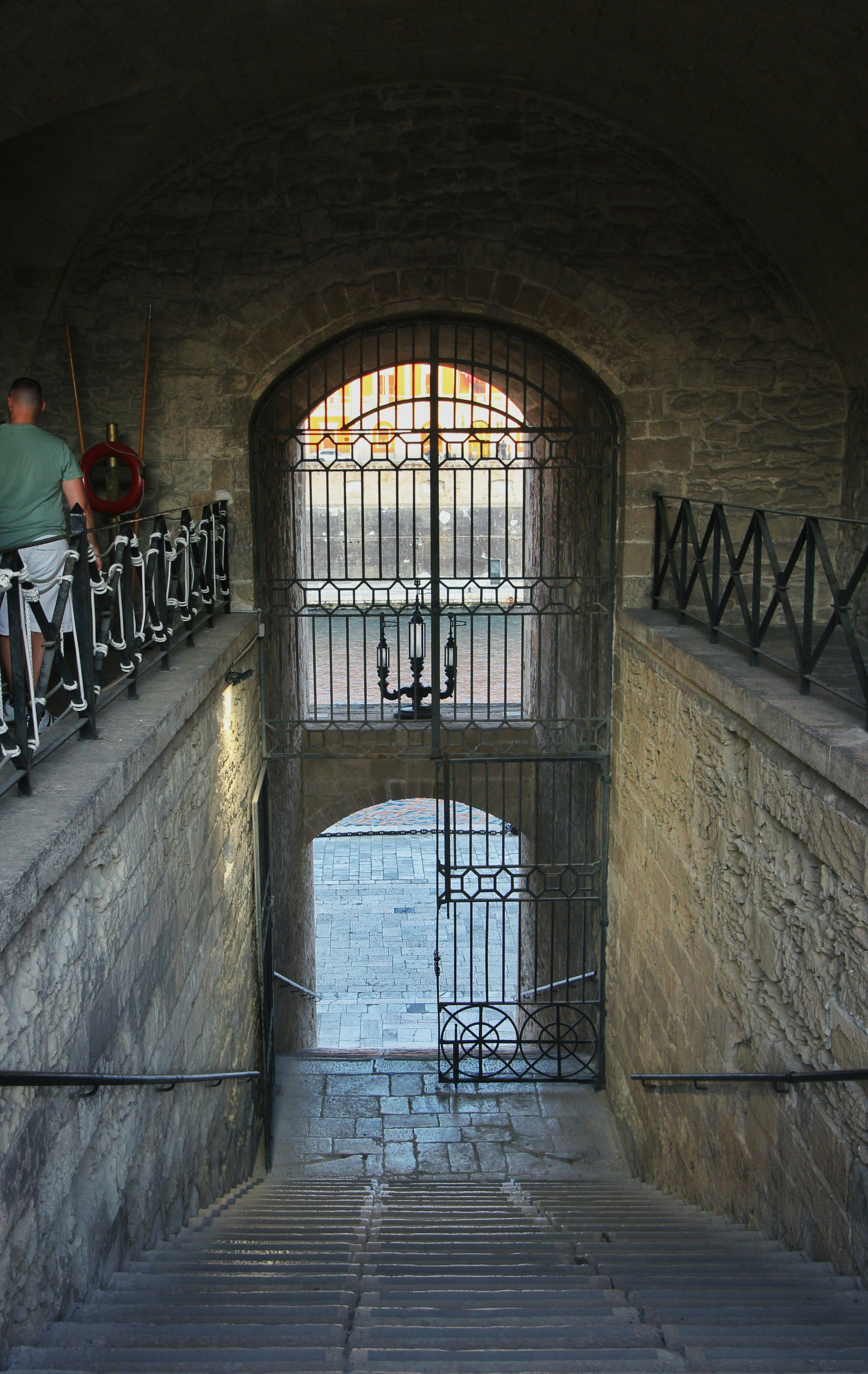 Stone stairway leading to a gated archway with sunlight illuminating the courtyard beyond.