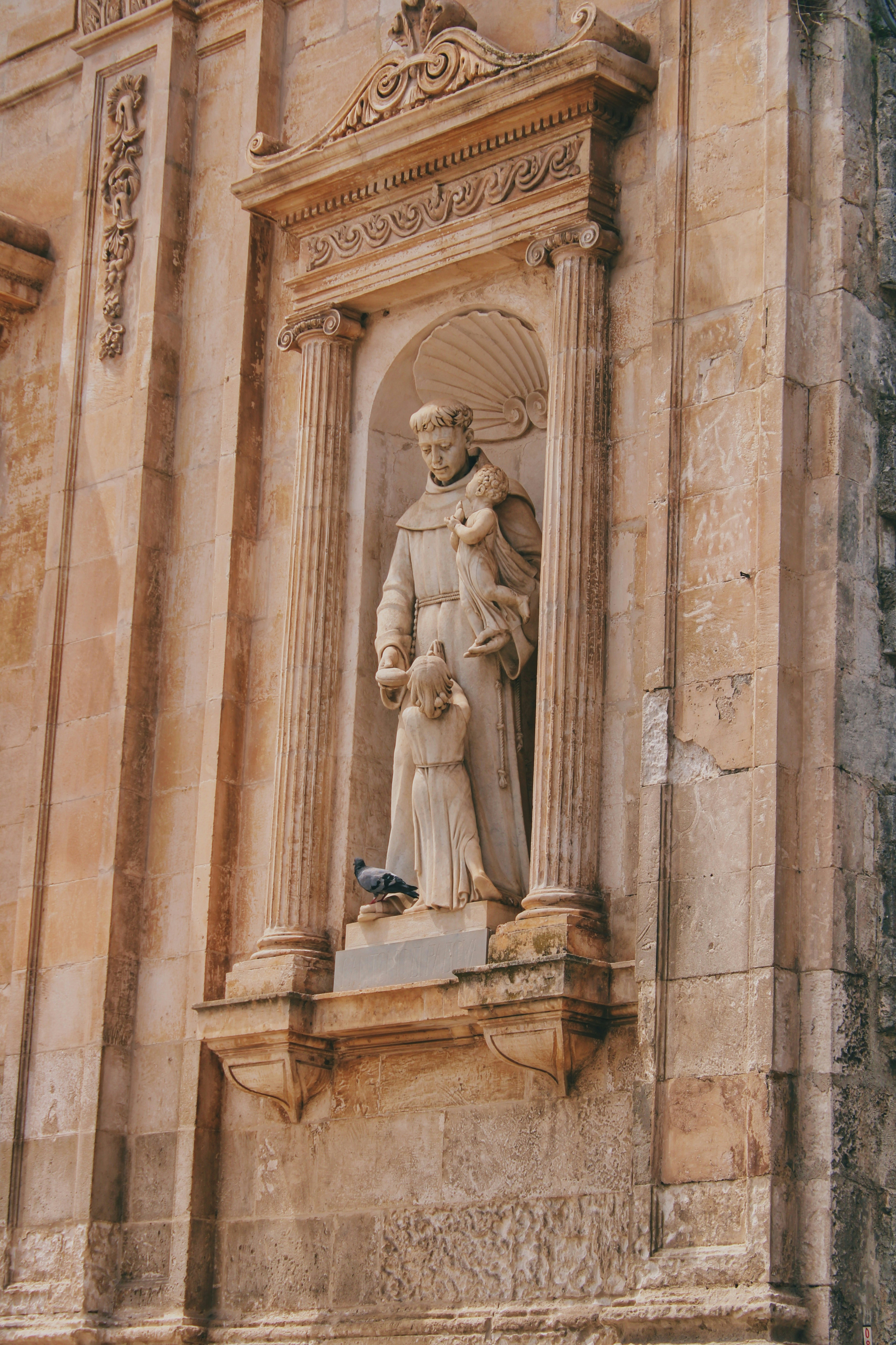 Saint in a Weathered Niche: Carved Archway and a Quiet Bird