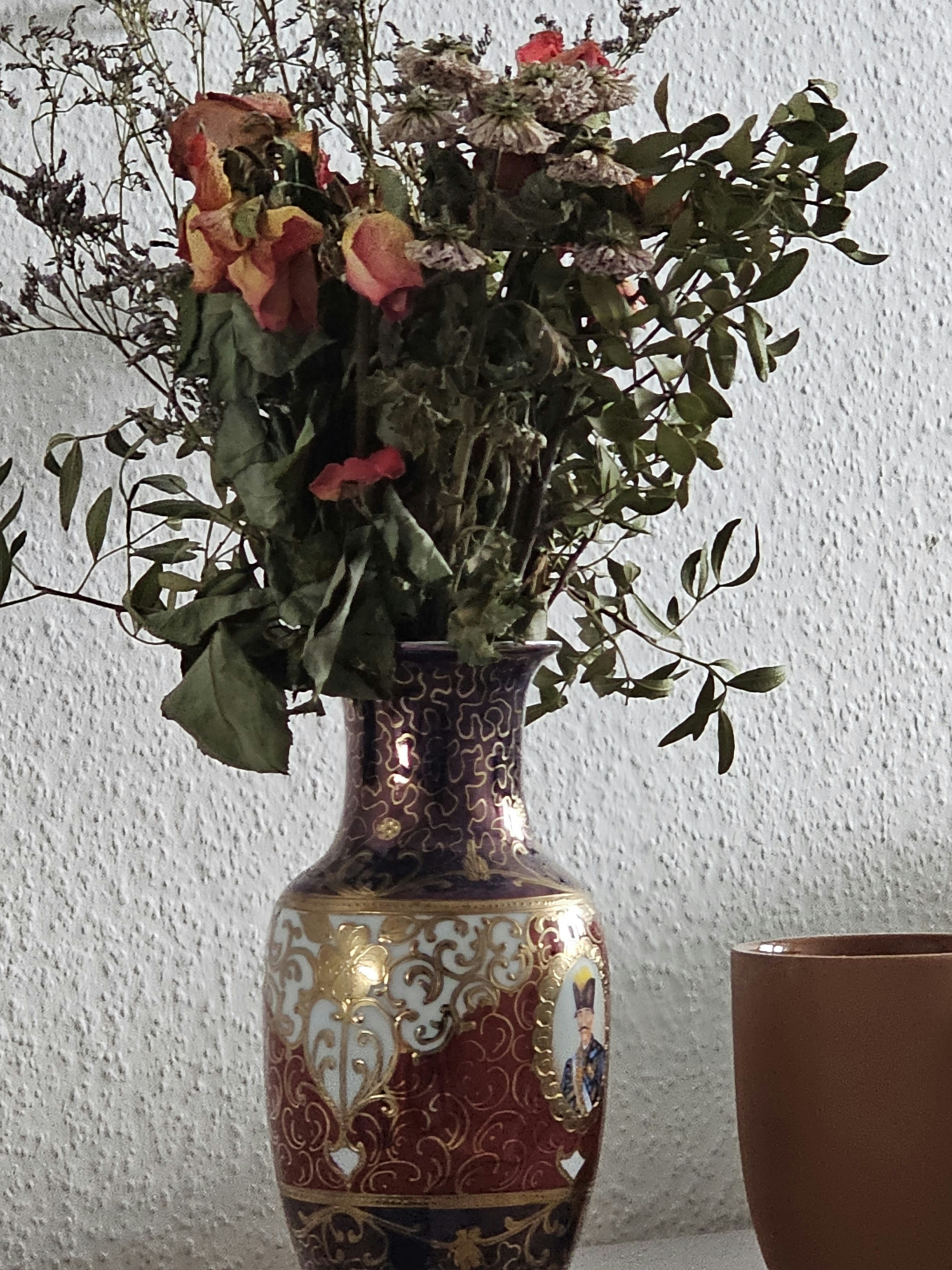 Ornate Porcelain Vase with a Faded Bouquet Against a Textured White Wall