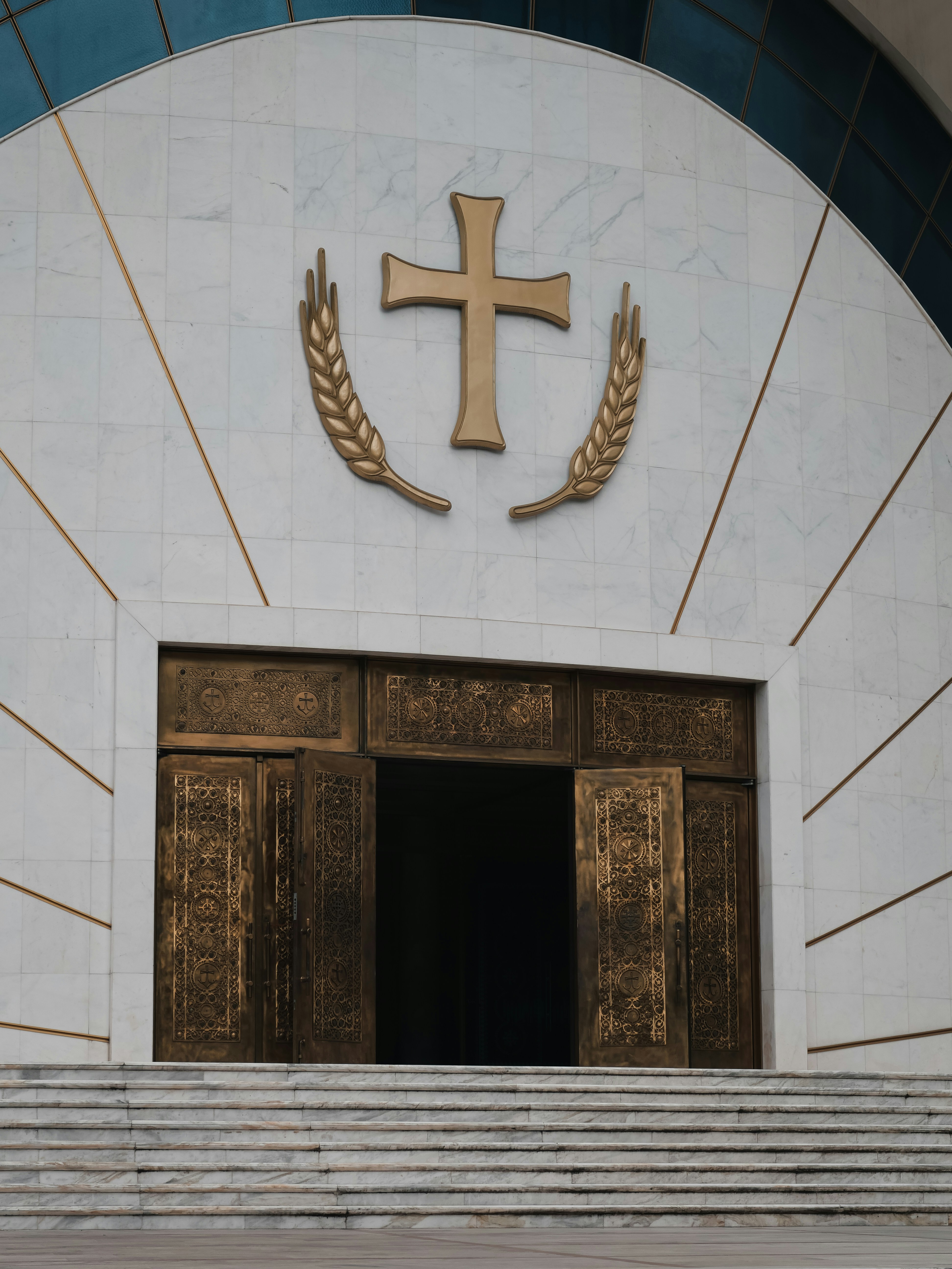 Laurel-Crowned Cross Framing a Bronze Door on Marble Facade