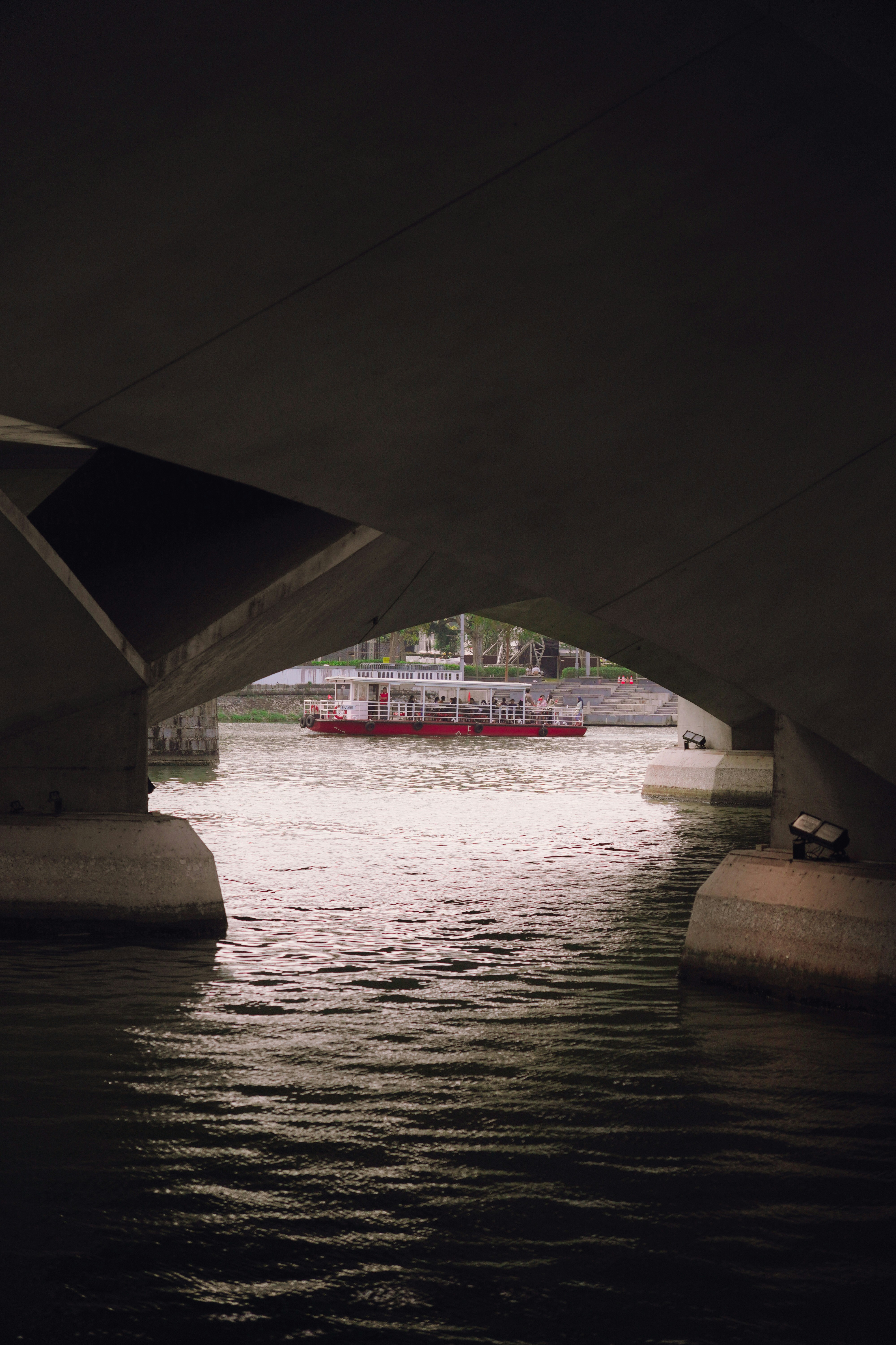 Through the Arch: A Red-Topped Riverboat Framed by Concrete Shadows