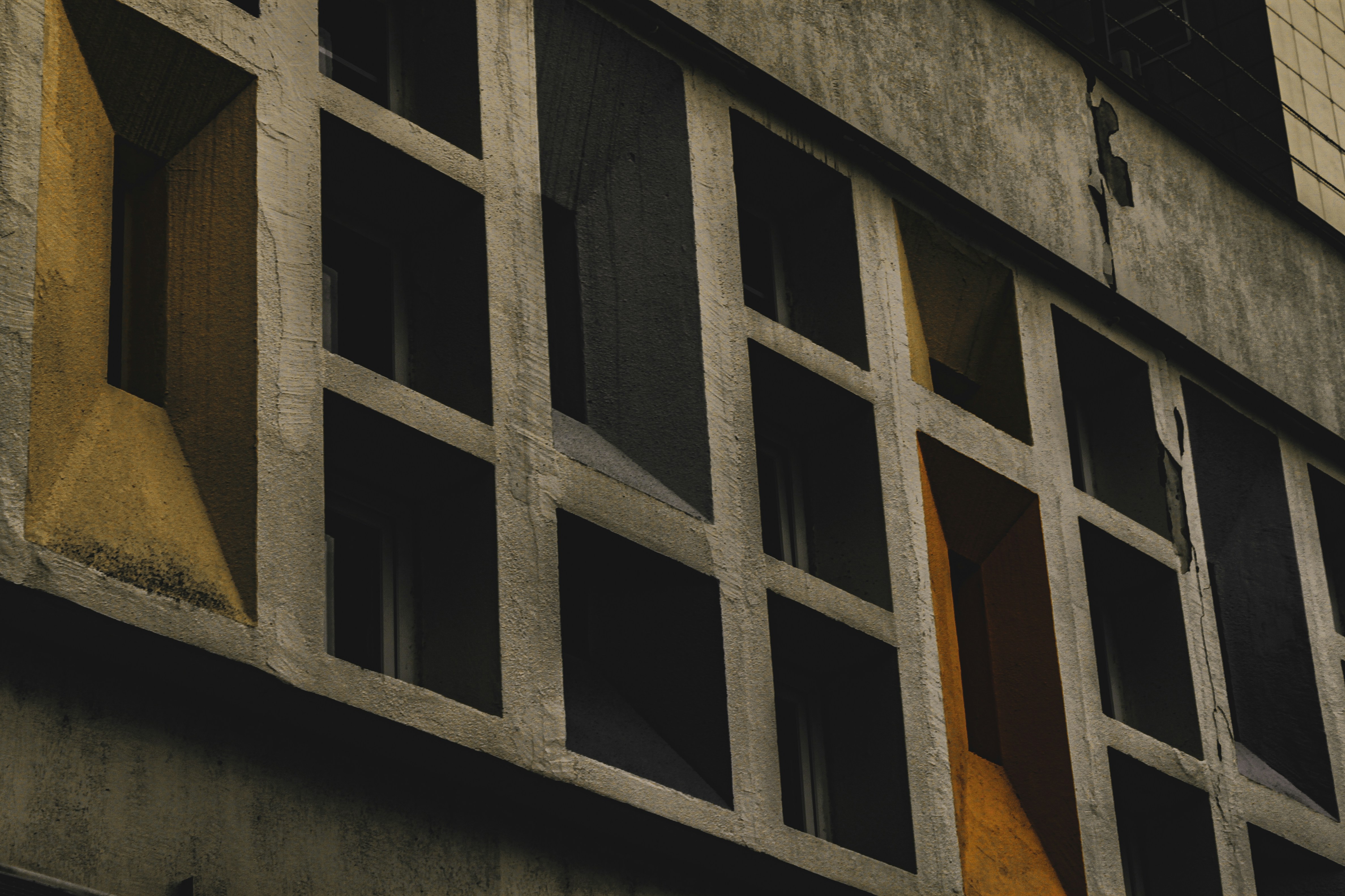 Geometric Echoes in a Weathered Facade: Yellow Slits Amid Concrete Grids