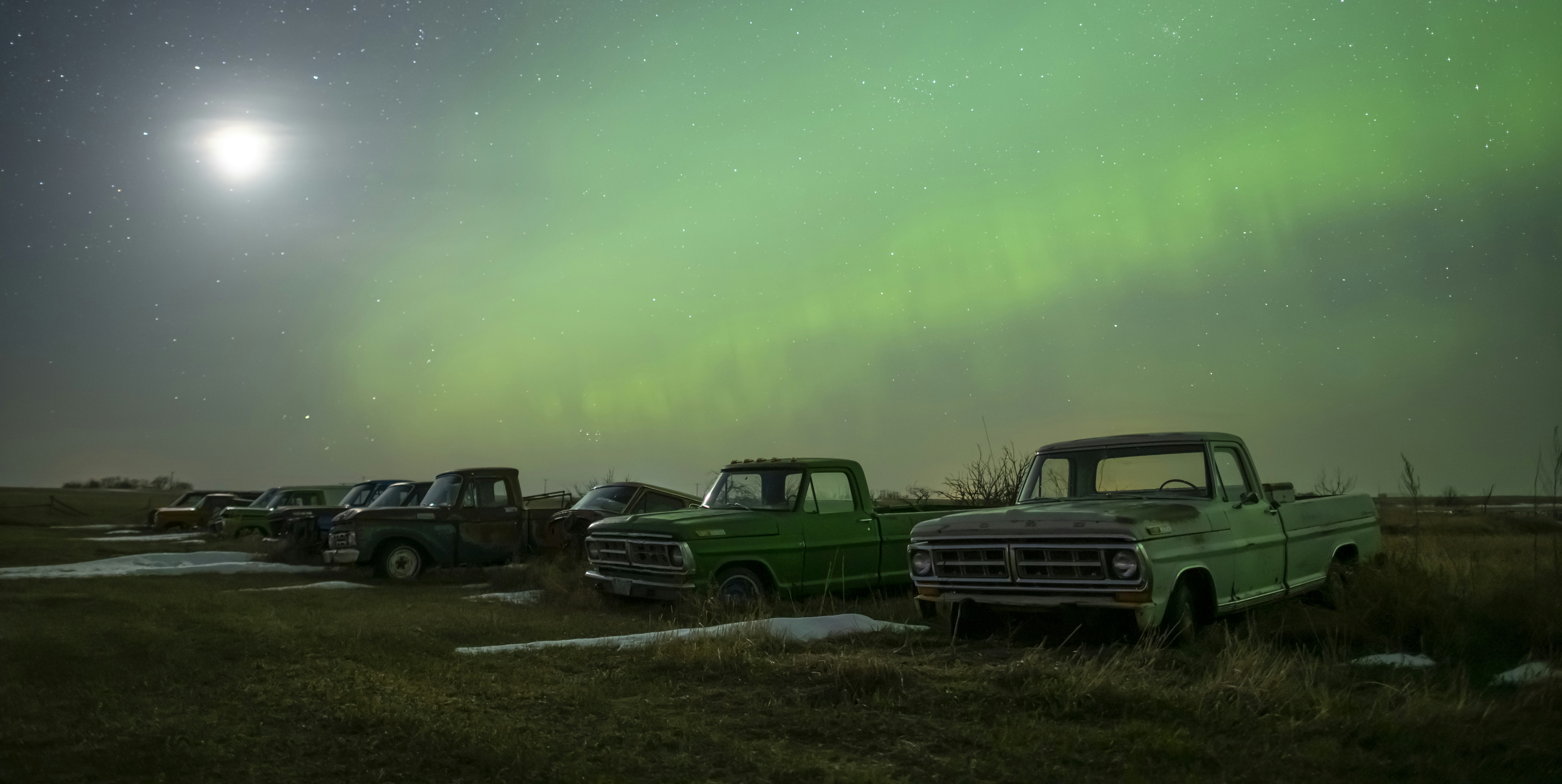 Aurora Over a Row of Weathered Pickups Beneath a Moonlit Night