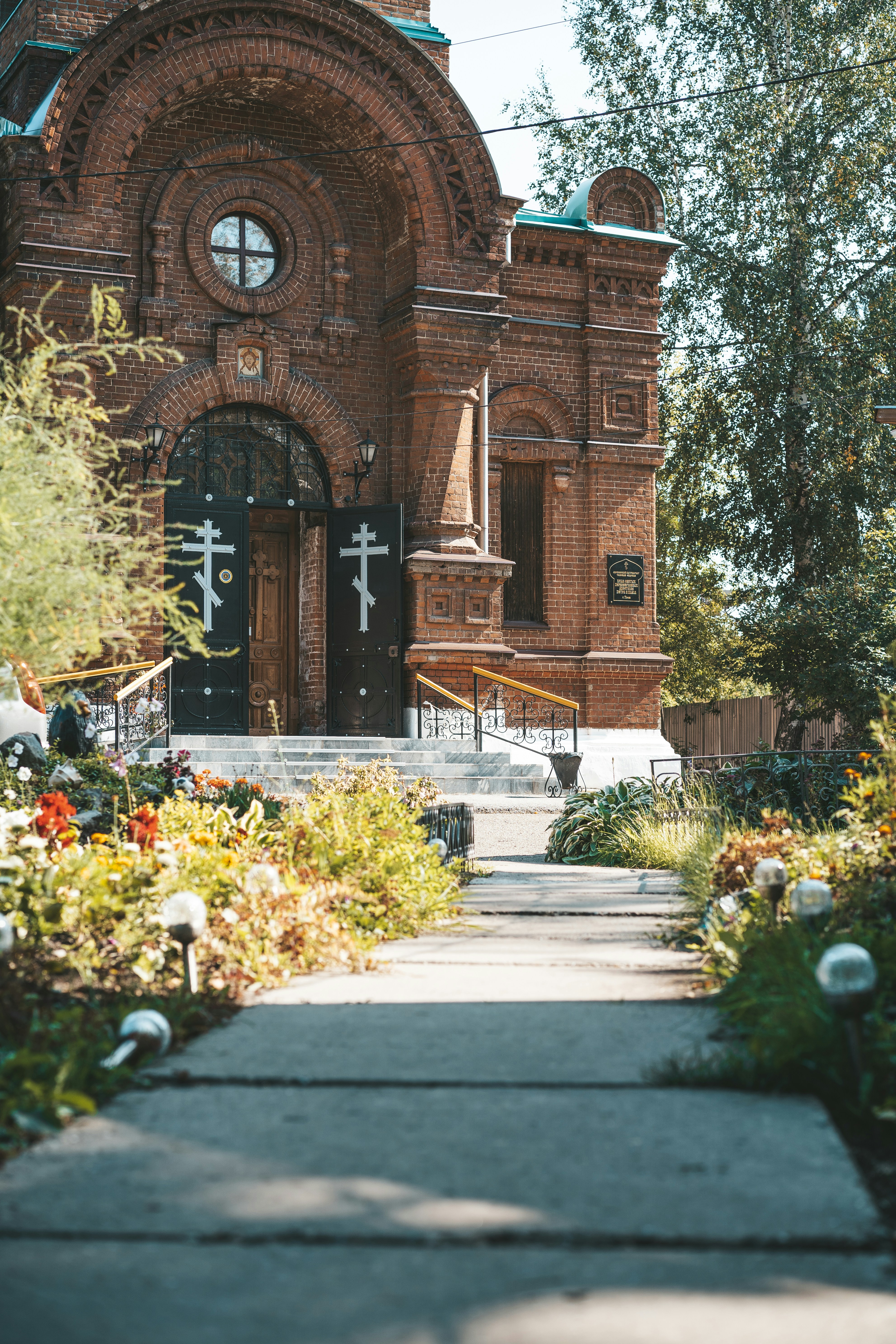 Sunlit Ascent to a Brick Orthodox Church Framed by a Blooming Path