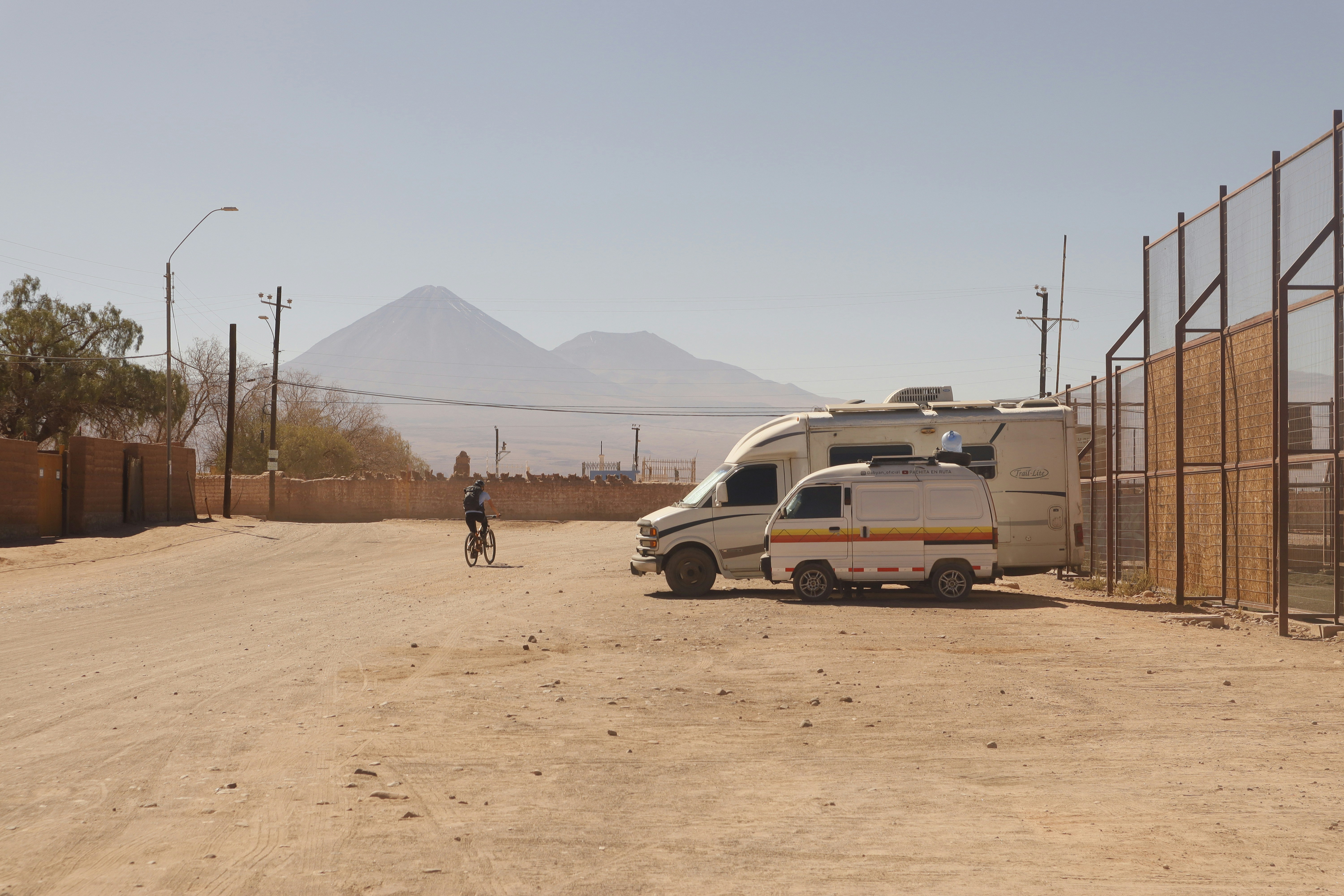 Desert Transit: Cyclist Near a Parked Camper Against a Mountain Horizon