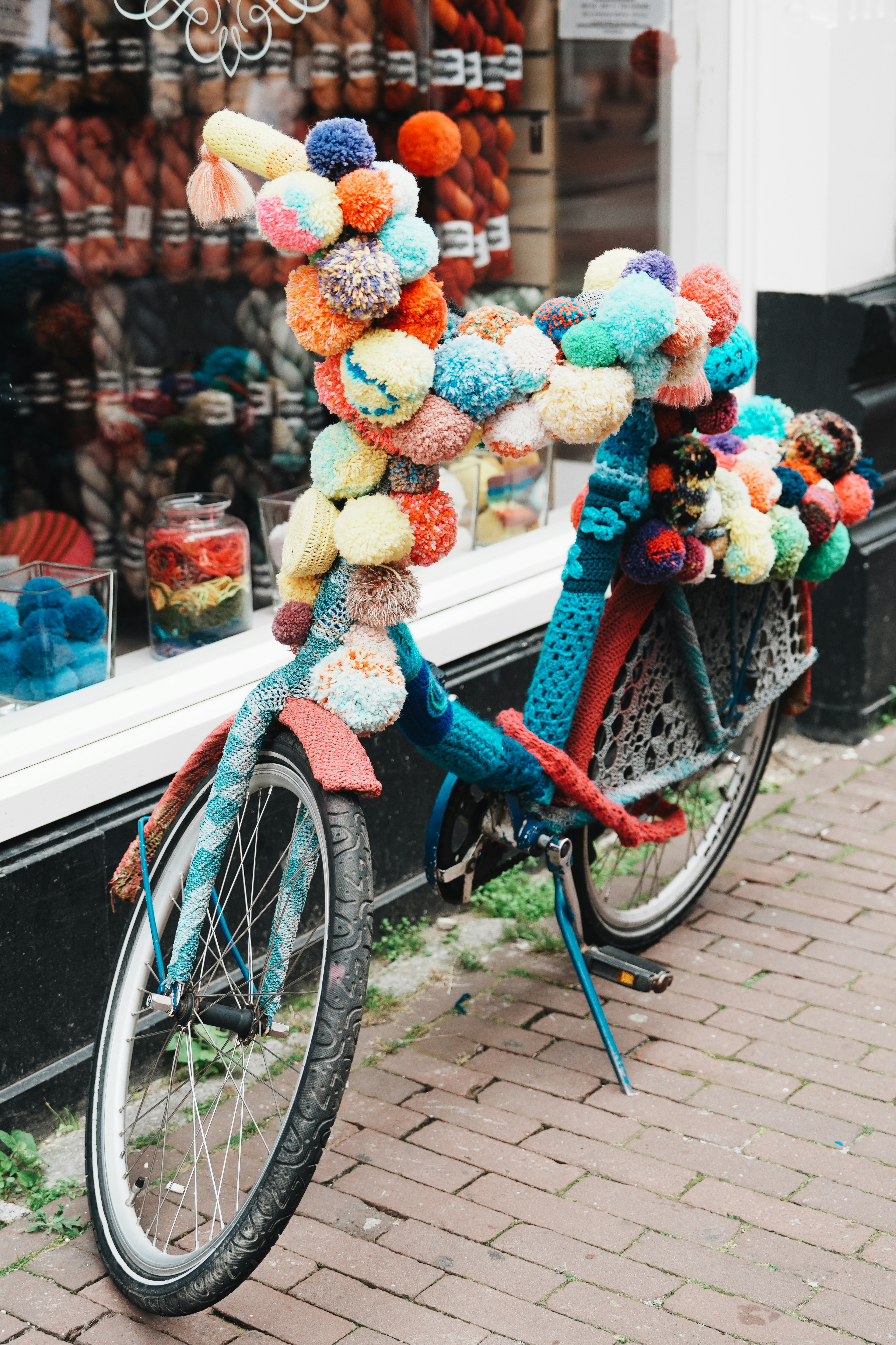 Pom-Pom Parade: A Bicycle Dressed in Colorful Yarn by a City Shopfront