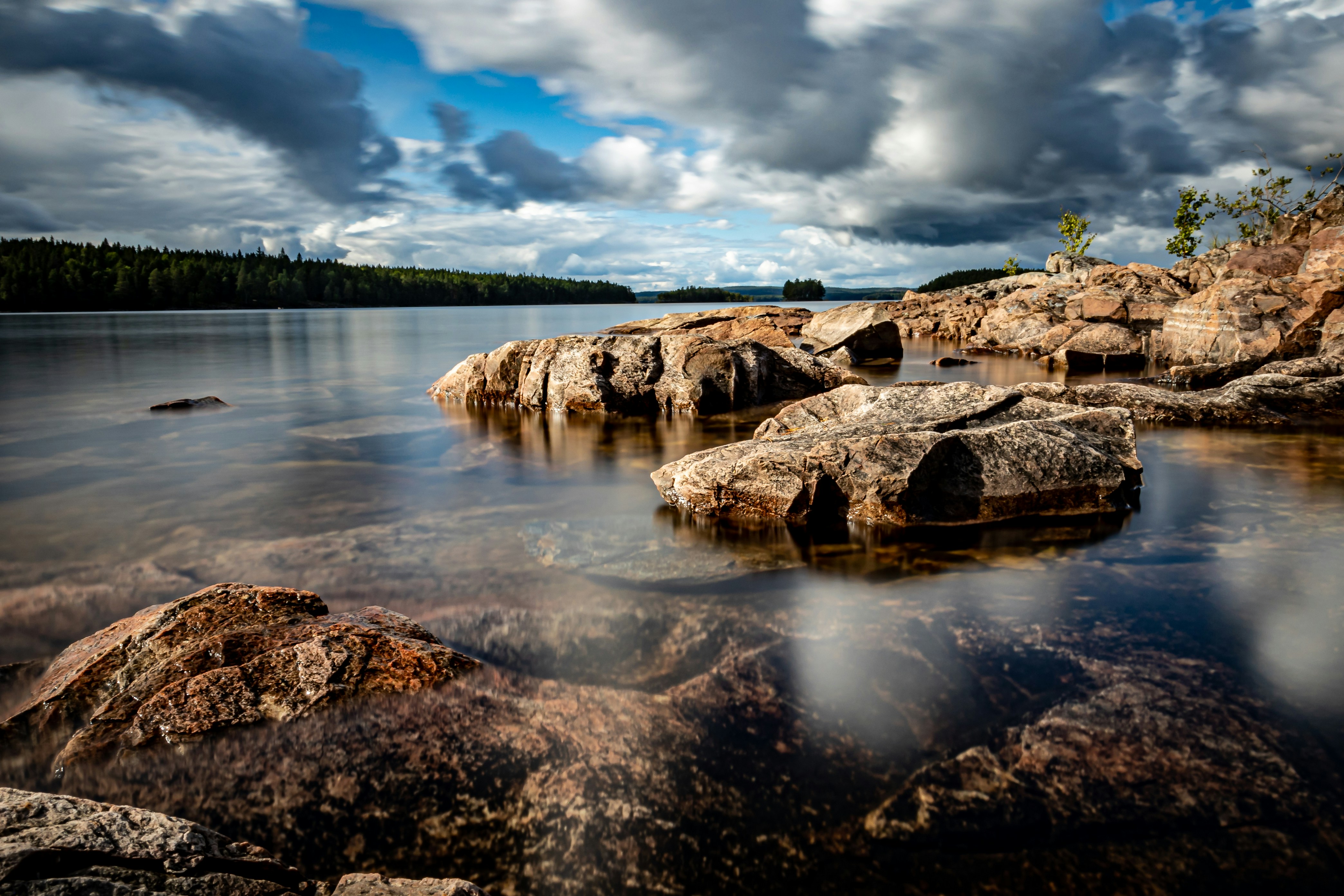A body of water surrounded by rocks under a cloudy sky photo – Free ...