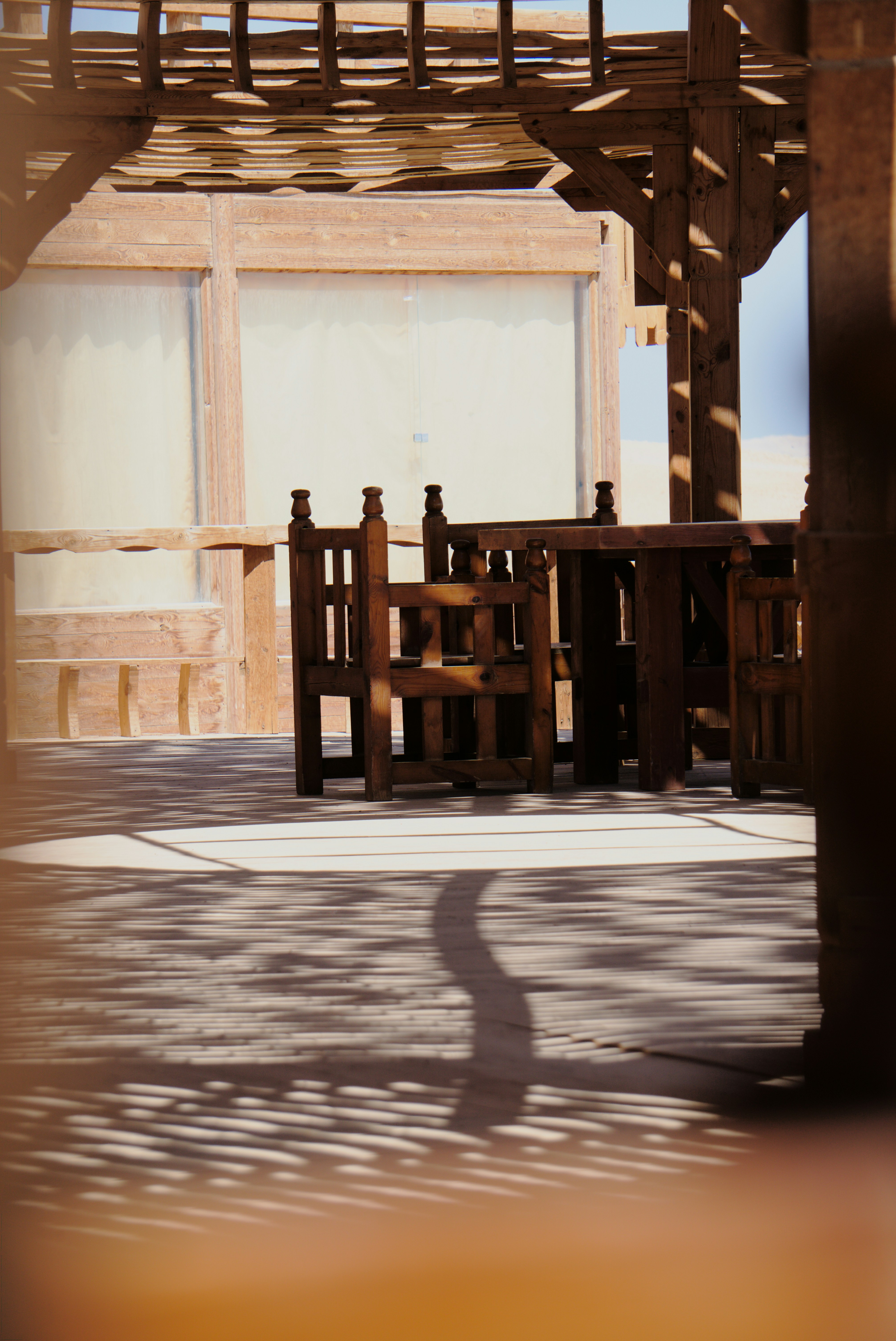 Lattice Shadows and Quiet Seating: Sunlit Veranda Table Under Wooden Beams