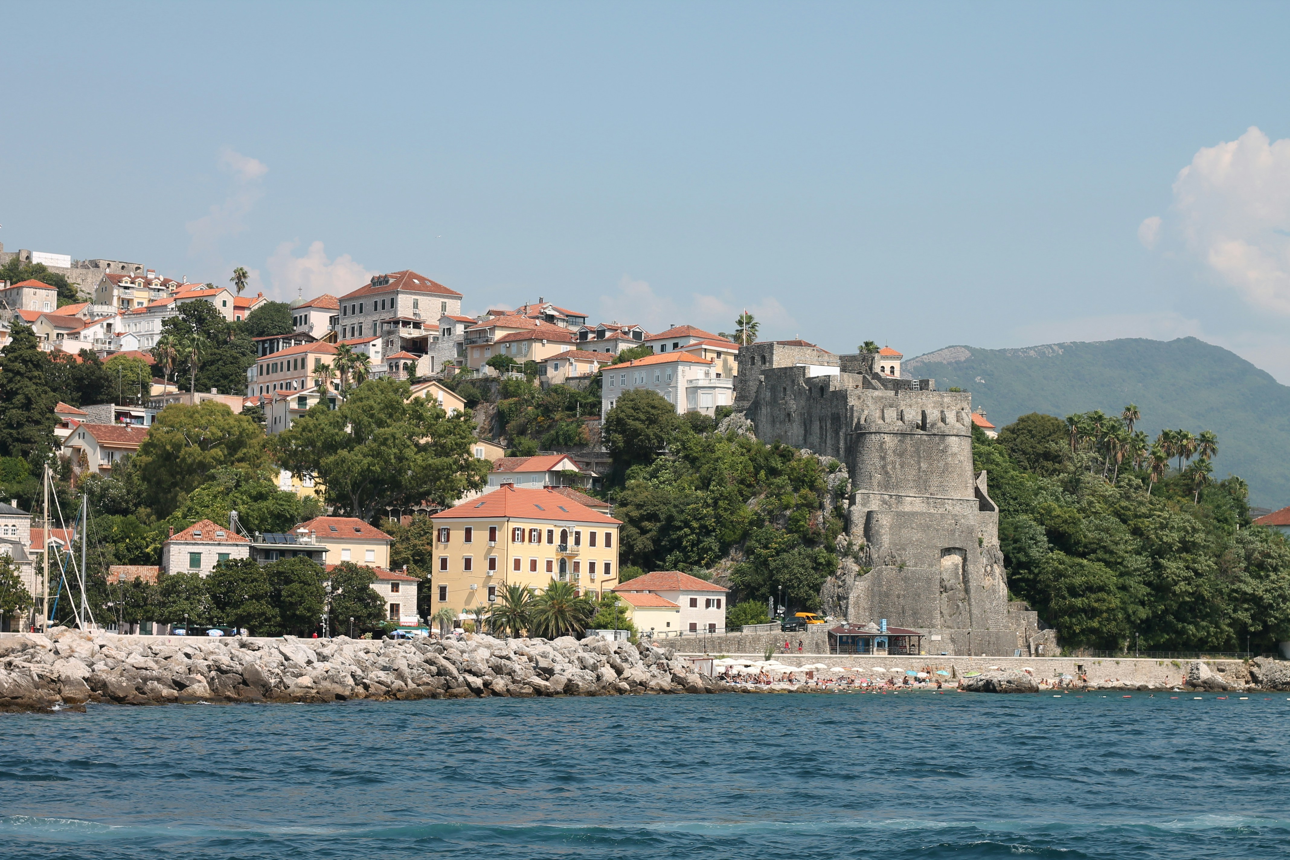 Hillside village with traditional houses and ancient stone tower by the sea under a clear blue sky.