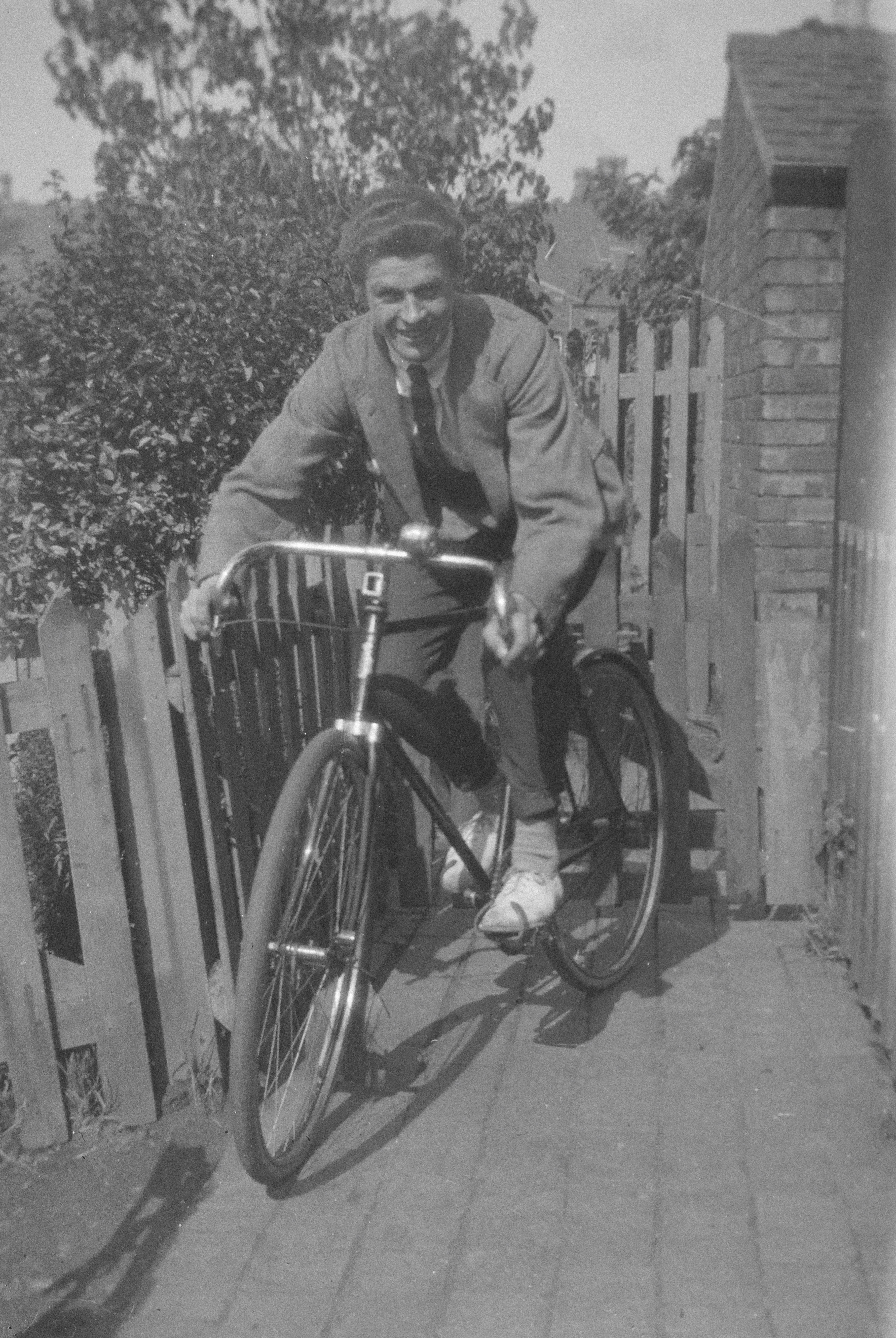 Dapper Cyclist on a Narrow Brick Path Between Garden Fences