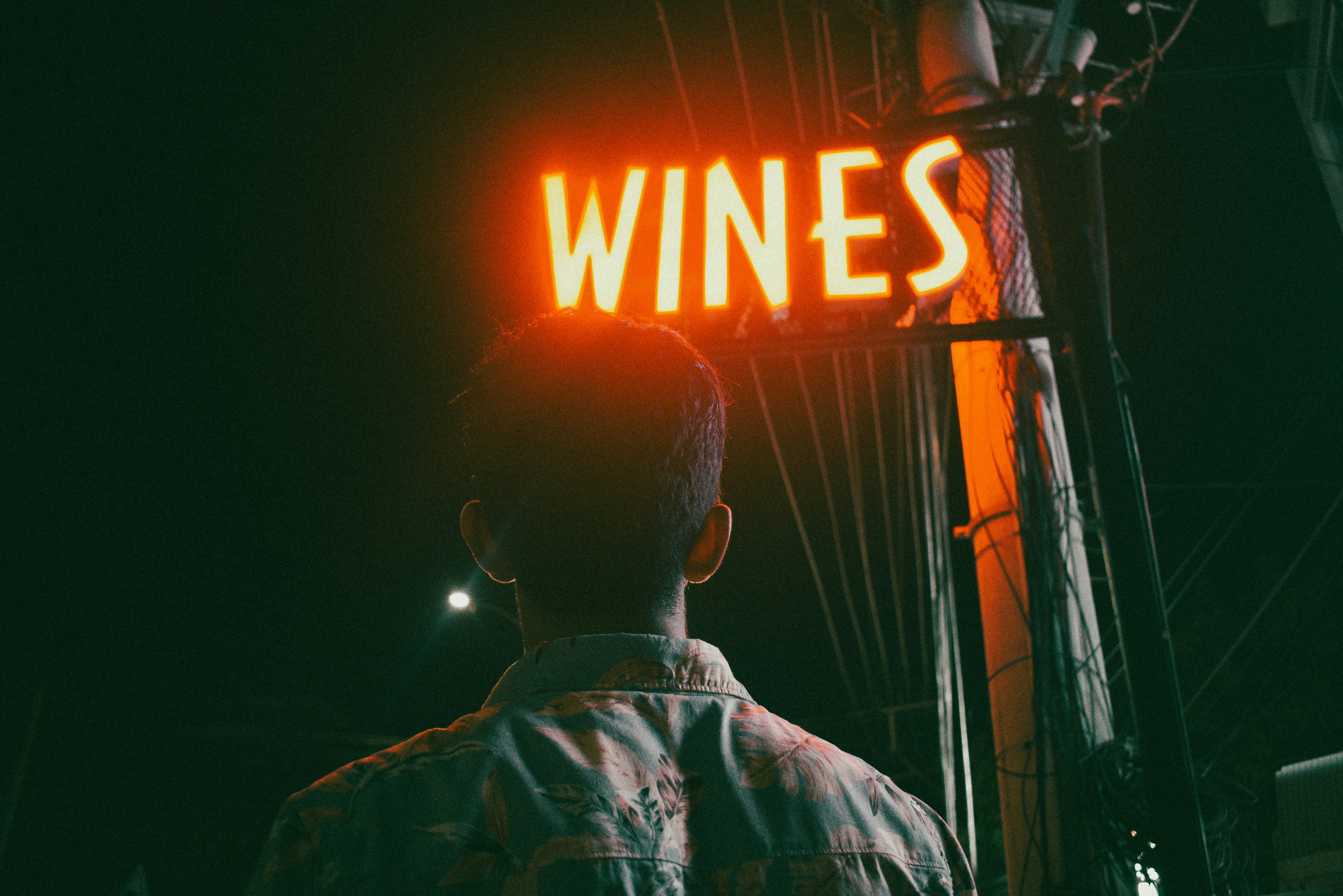 Person standing under a glowing neon 'WINES' sign at night.