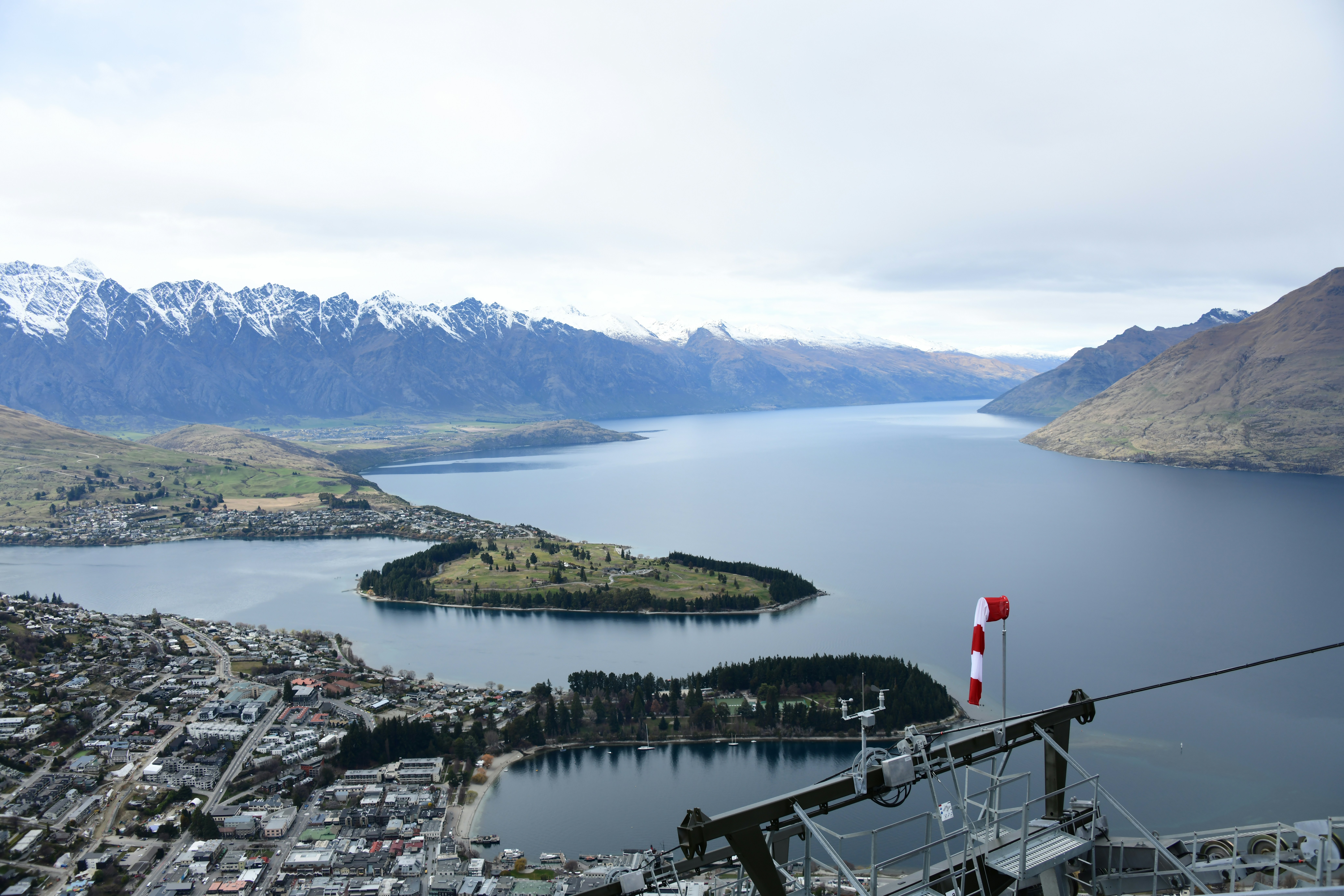 Aerial overlook: harbor, town, and snow-capped peaks from a crane