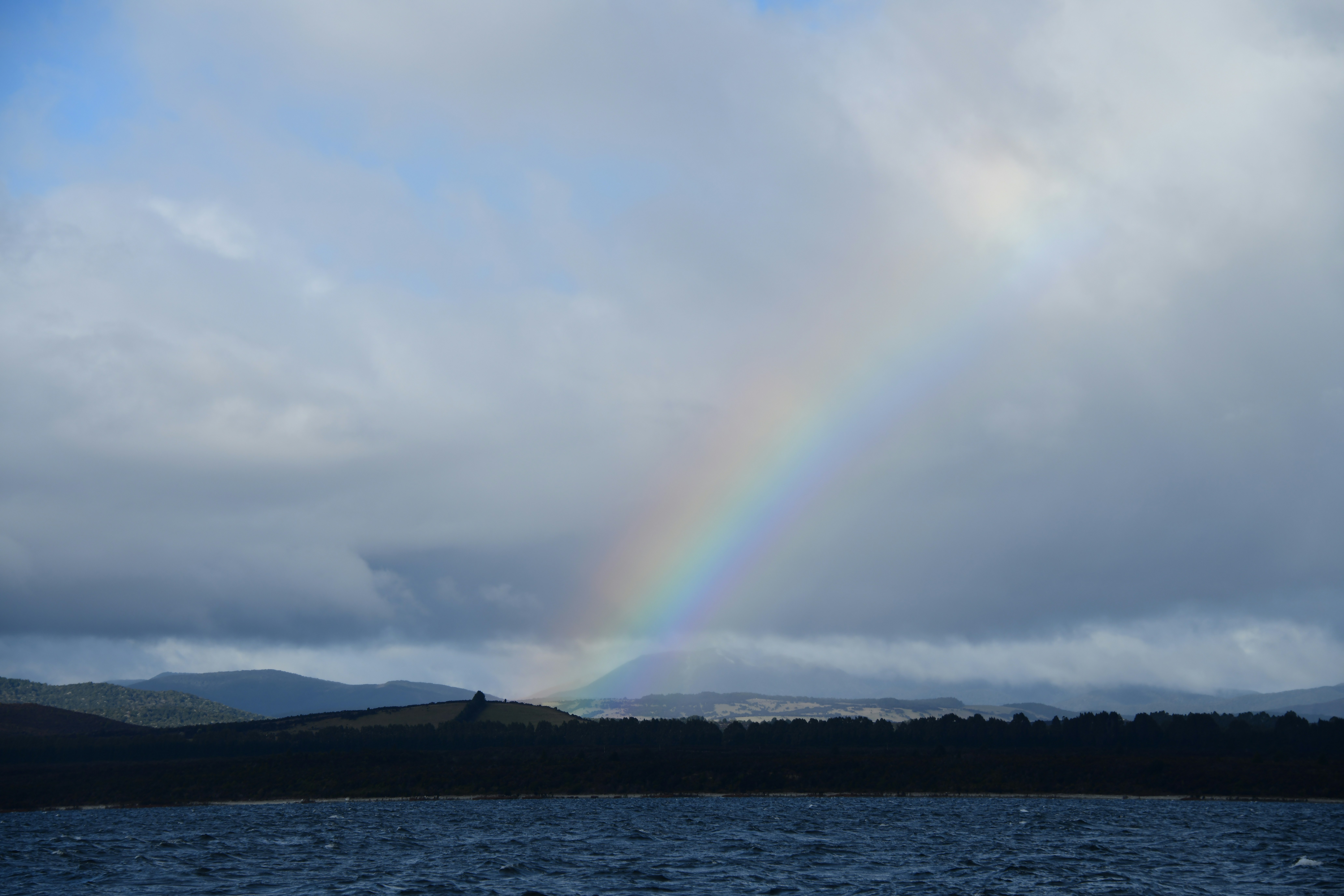 Rainbow arching above a calm lake beneath a cloudy sky.