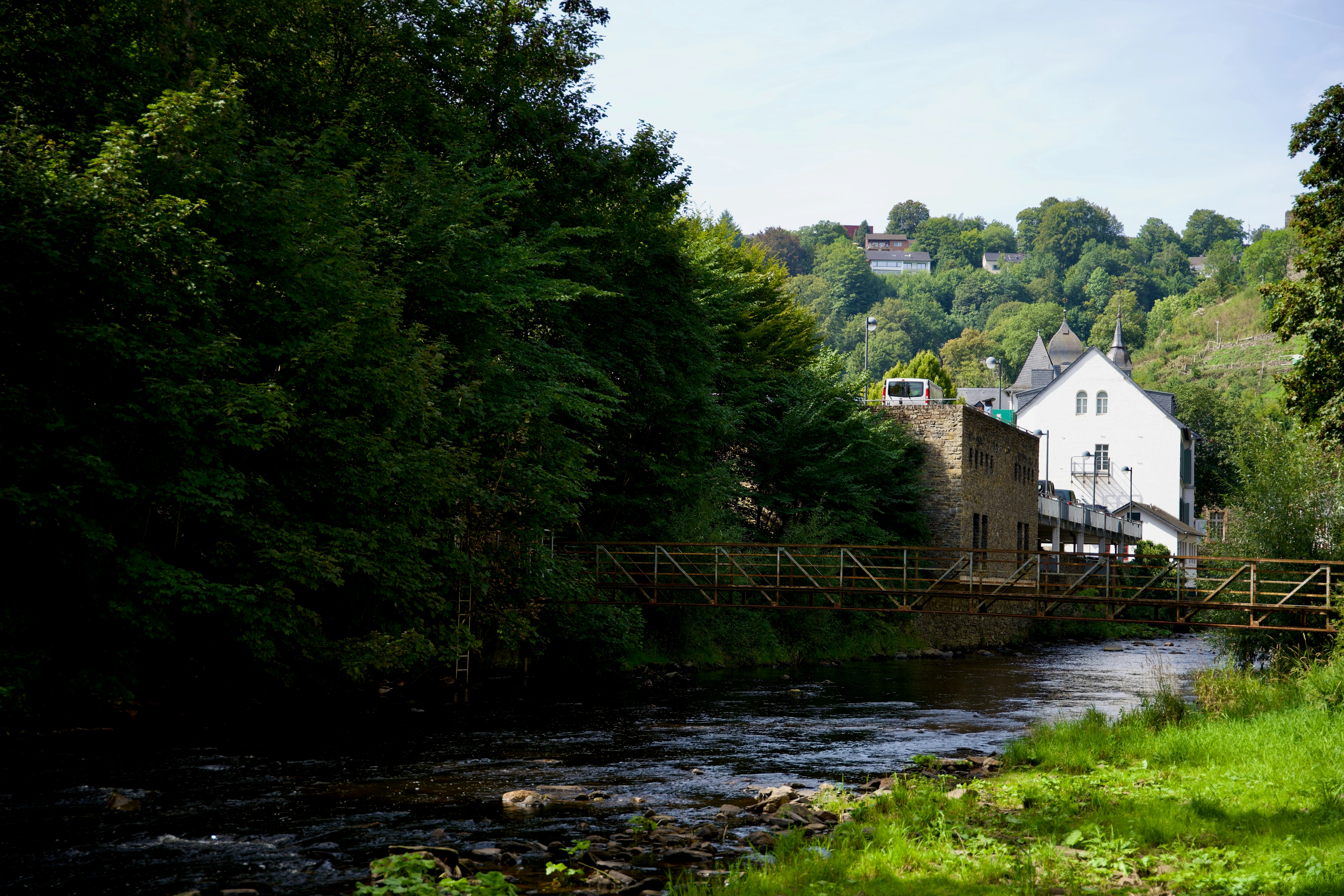 Serene river flowing past a rustic building and lush greenery under a clear sky.
