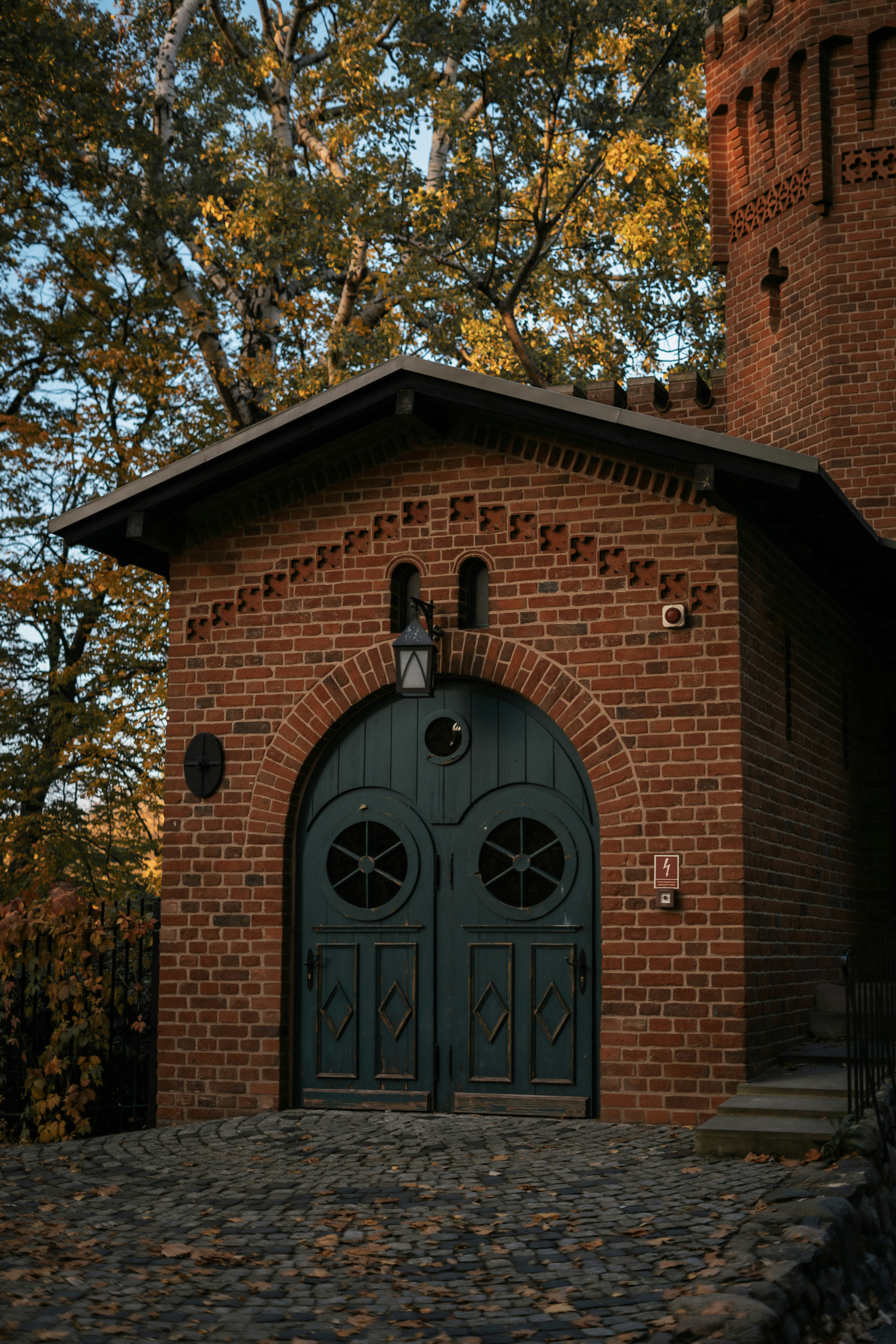 Teal-arched Doors in a Brick Gatehouse Under Autumn Light