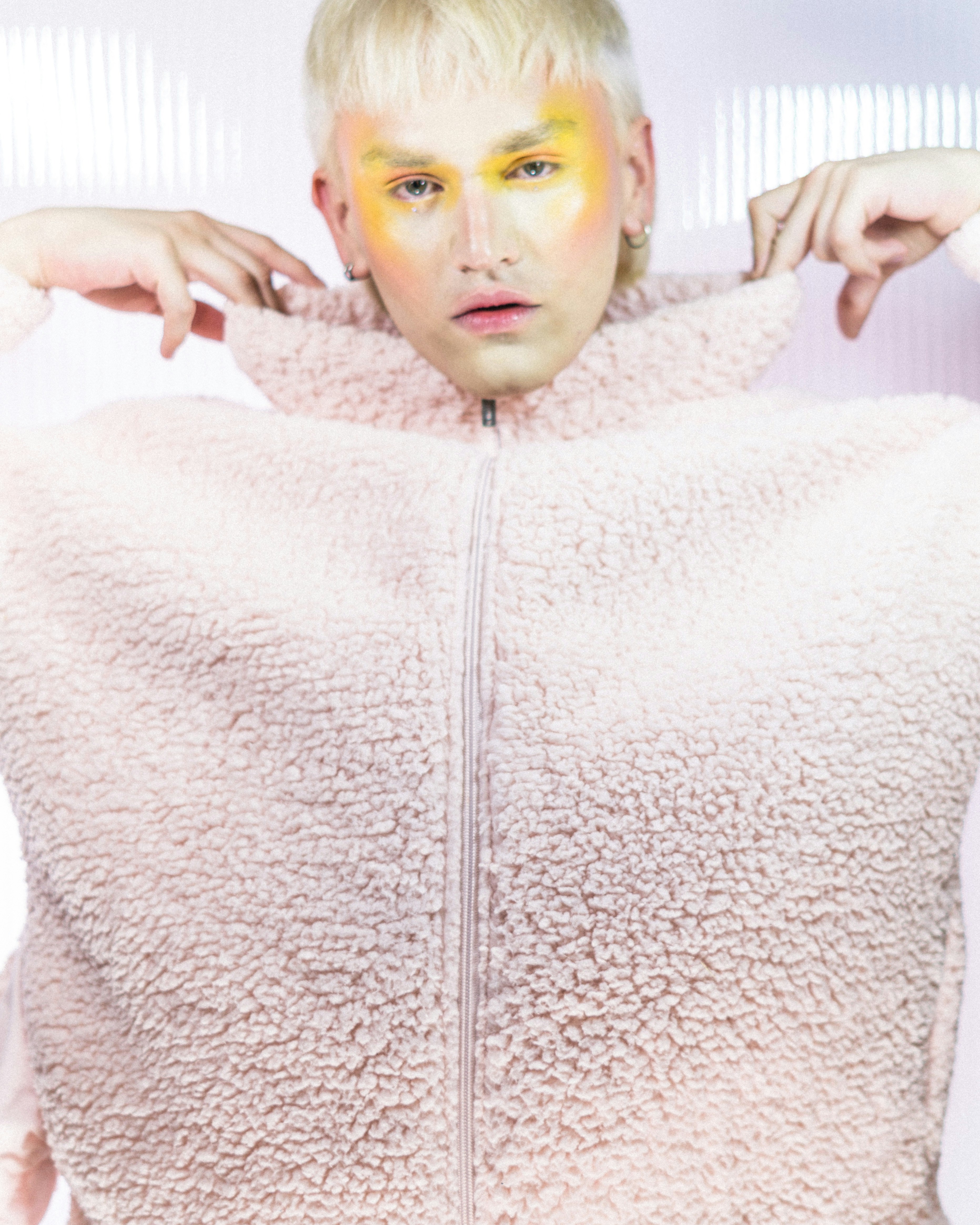 Model in oversized pink fleece jacket, featuring bold face makeup that contrasts with the soft fabric. The background adds a subtle glow, enhancing the overall aesthetic.