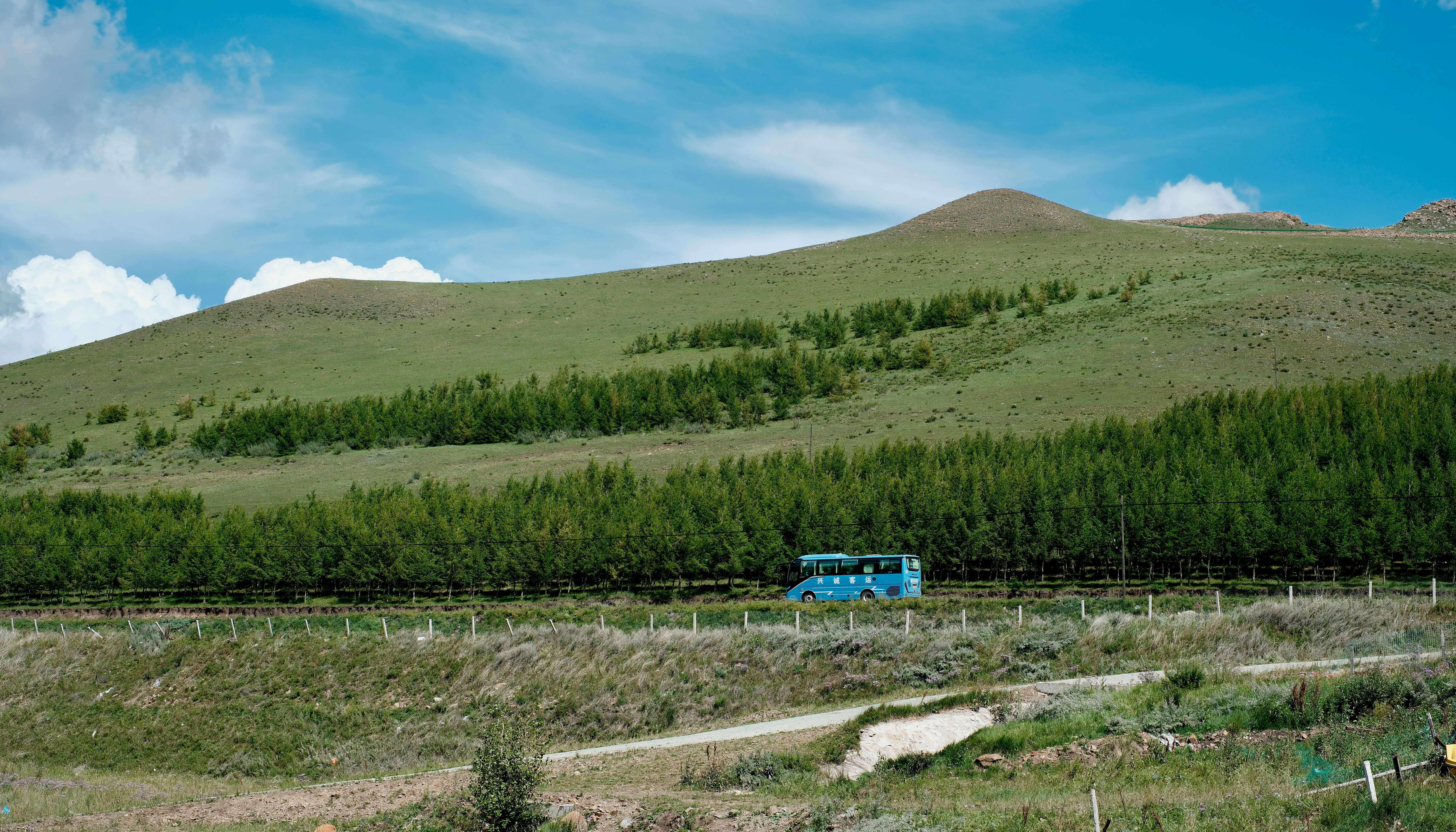 Blue Bus on a Narrow Track Through Rolling Prairies Under a Clear Blue Sky