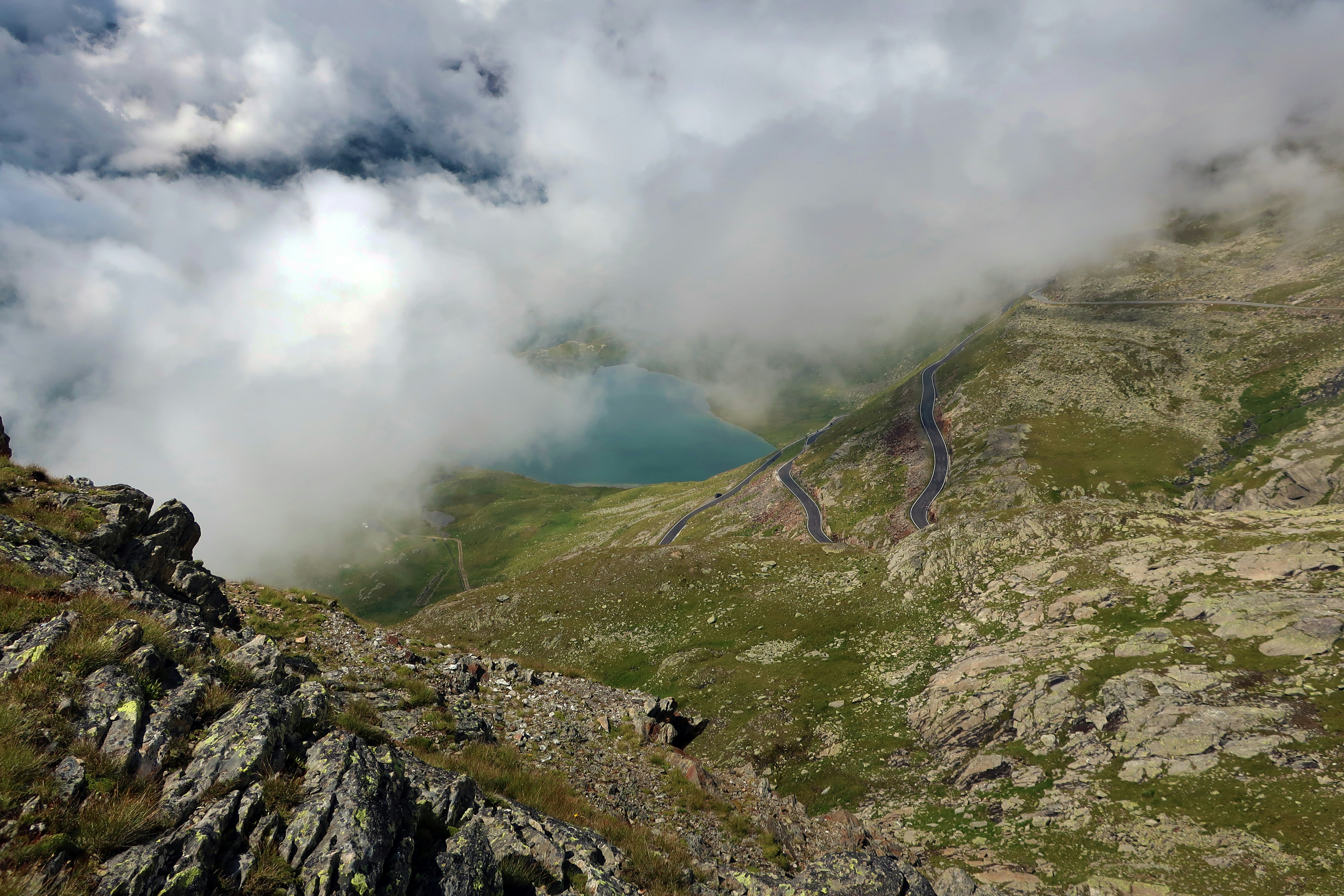 Rocky mountain landscape partially shrouded in clouds with a distant lake visible in the valley.