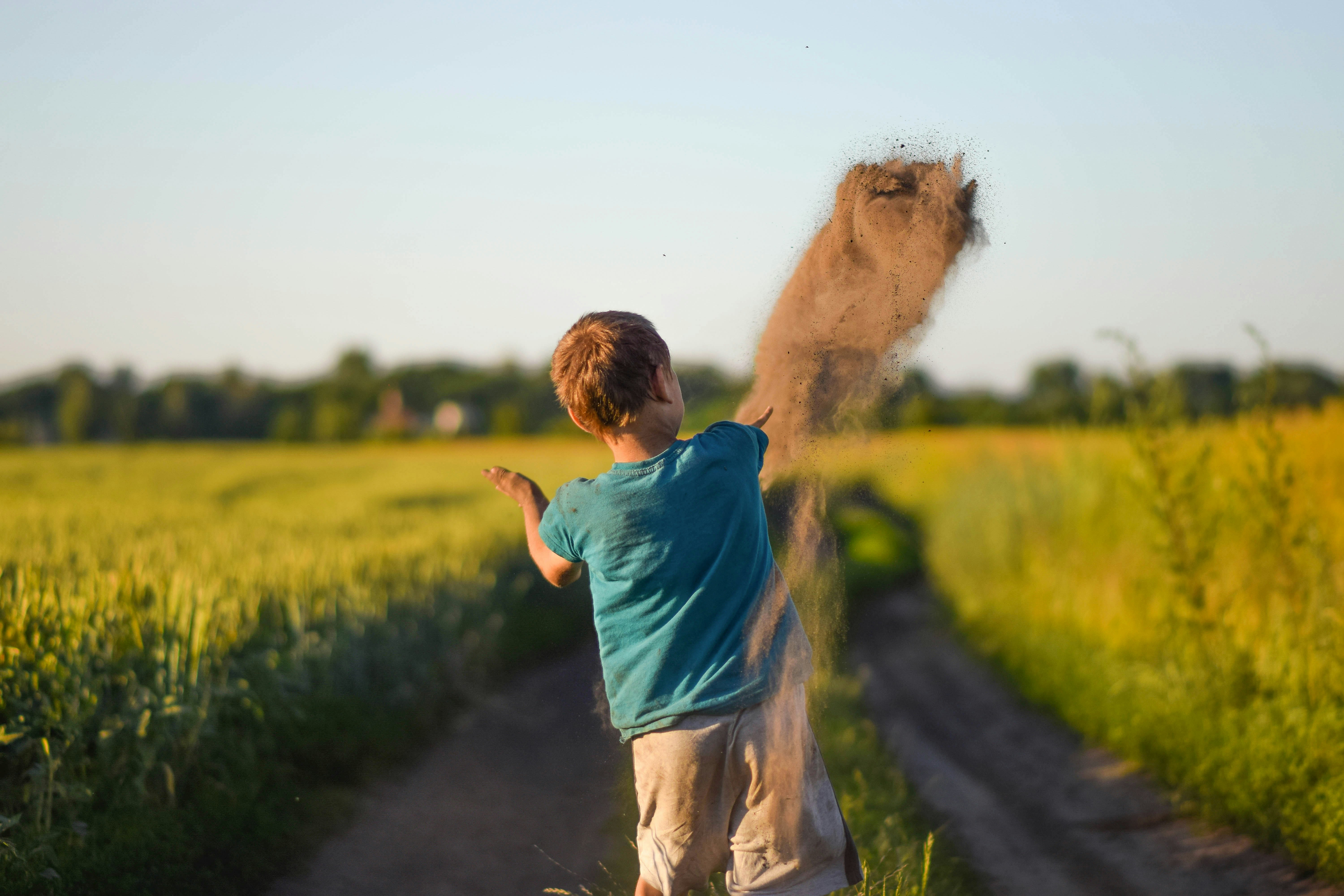 A young boy throwing sand on a dirt road photo – Free Boy Image on Unsplash