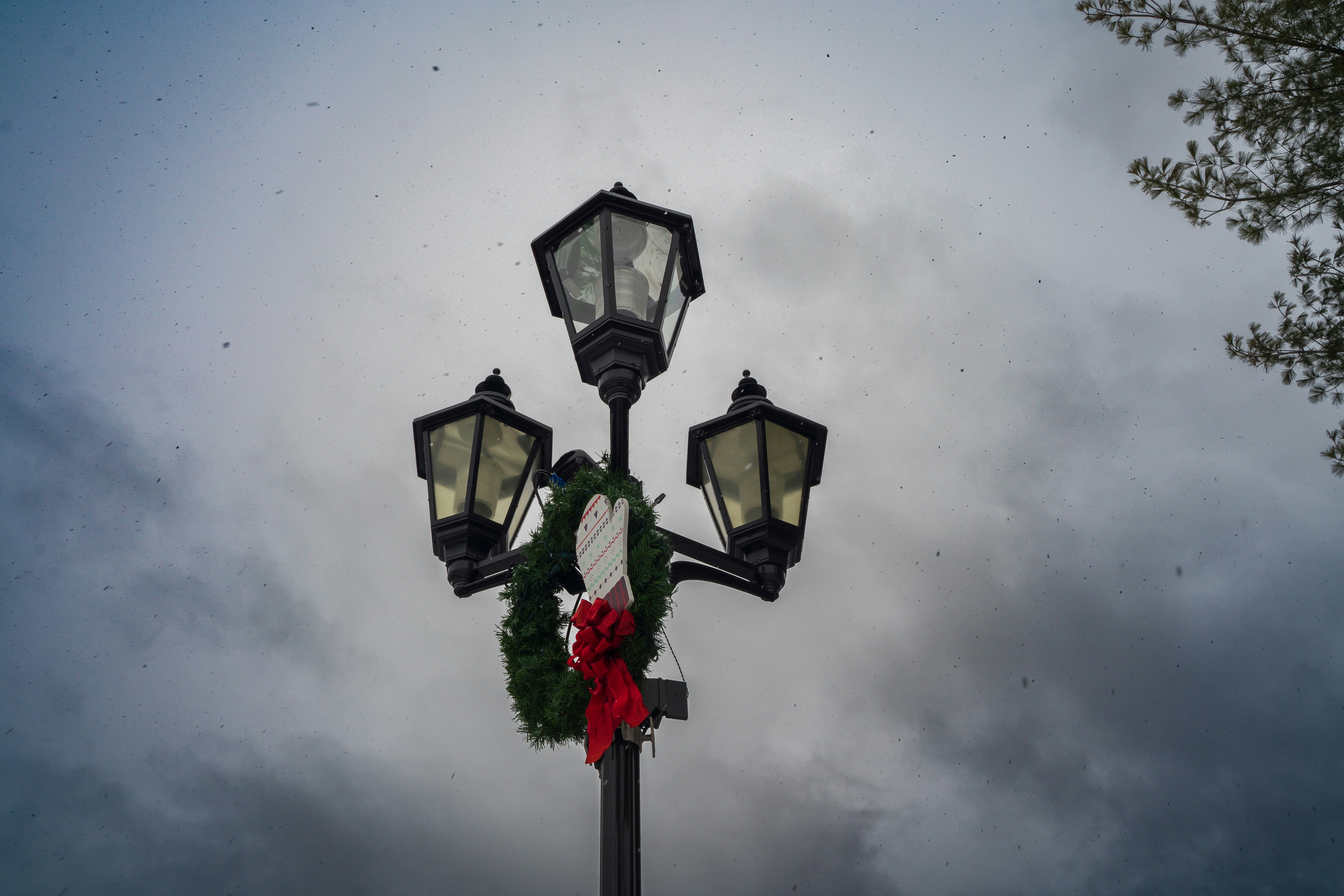 Three Lanterns, One Wreath: A Holiday Lamppost Beneath a Cloudy Winter Sky