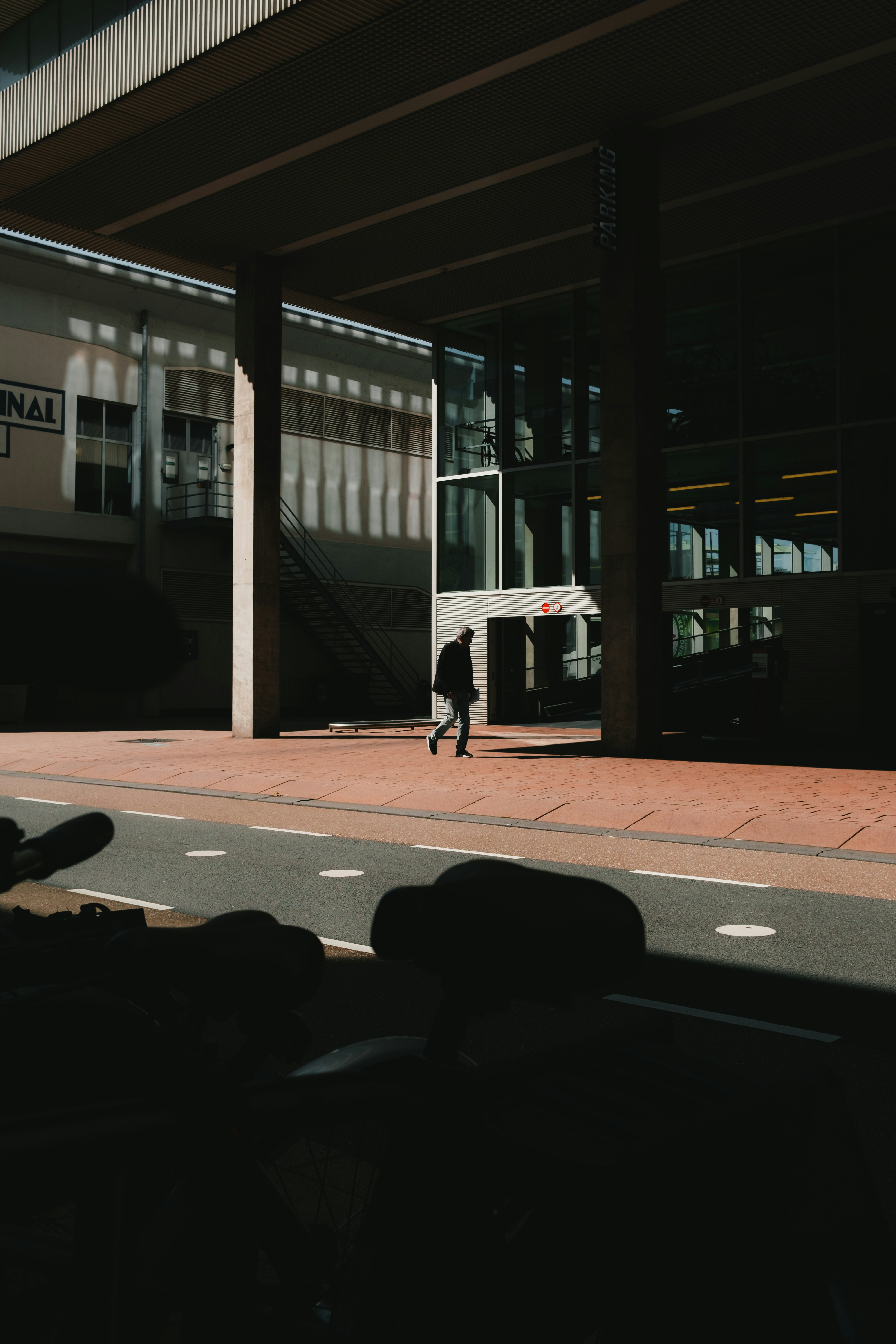 A man walking down a street next to a tall building photo – Free Street ...