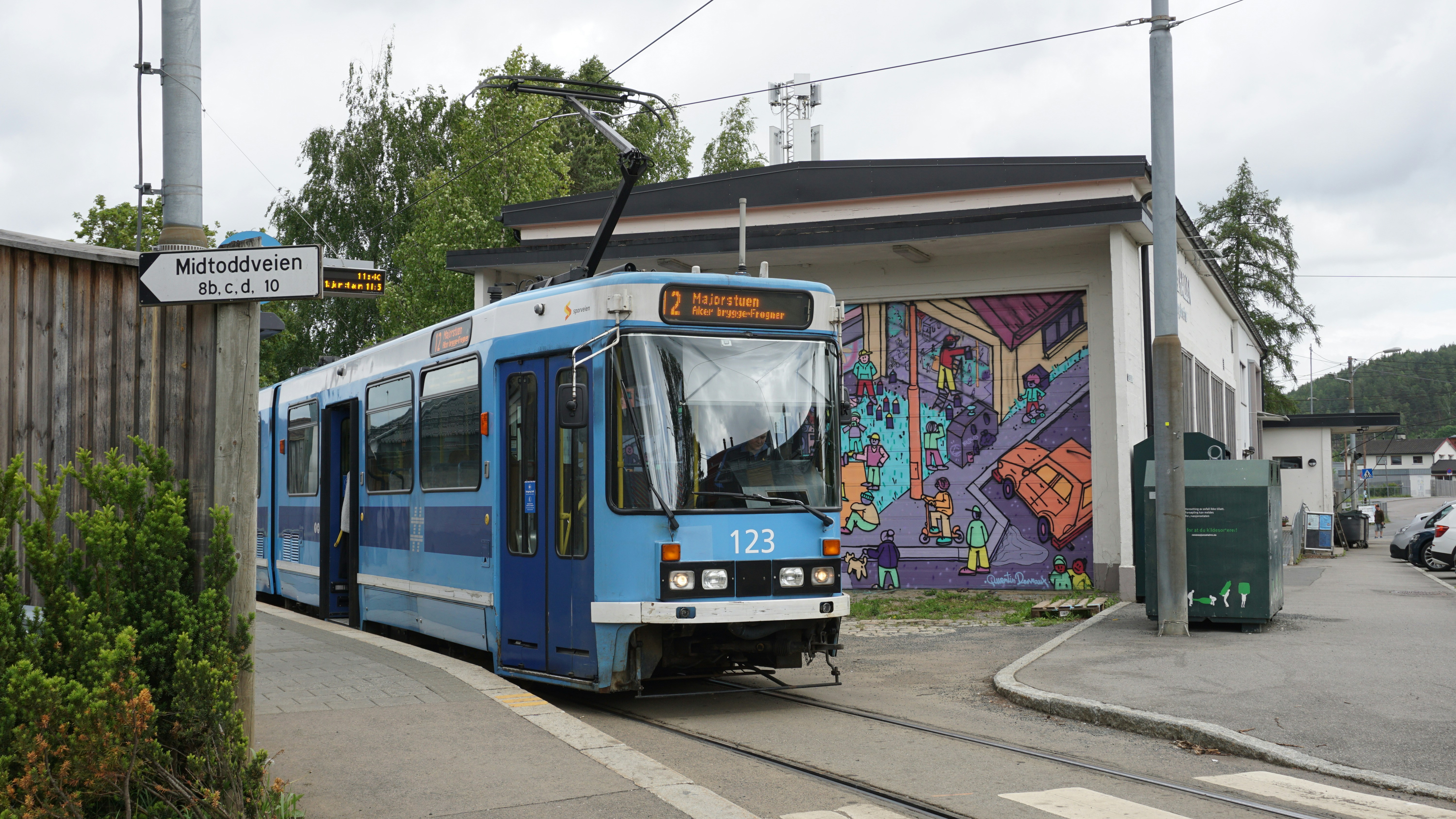 Blue Tram Glides by a Mural-Lined Wall on a Quiet Street Corner