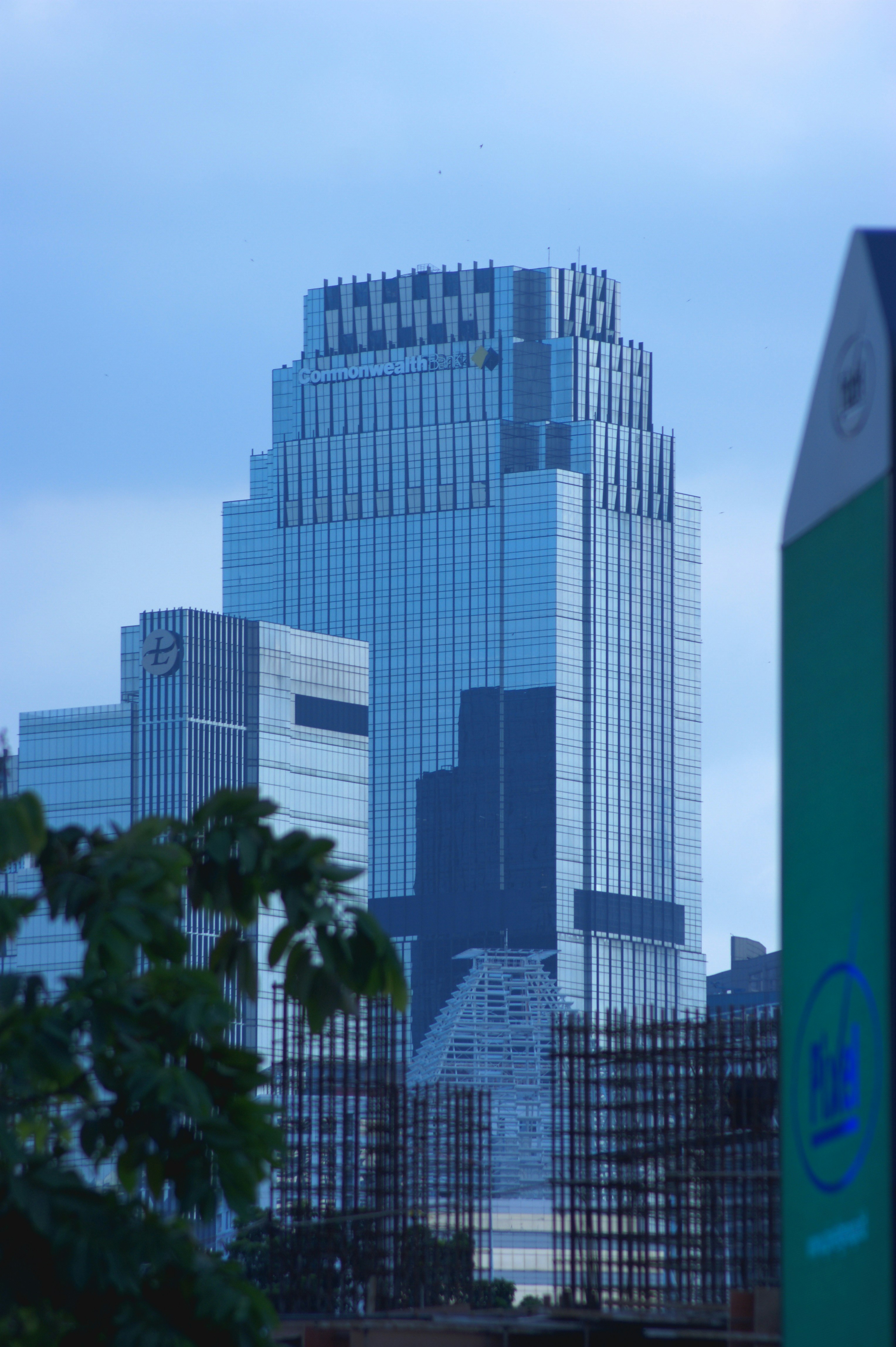 Tall glass skyscraper reflecting the sky, surrounded by urban structures and greenery.