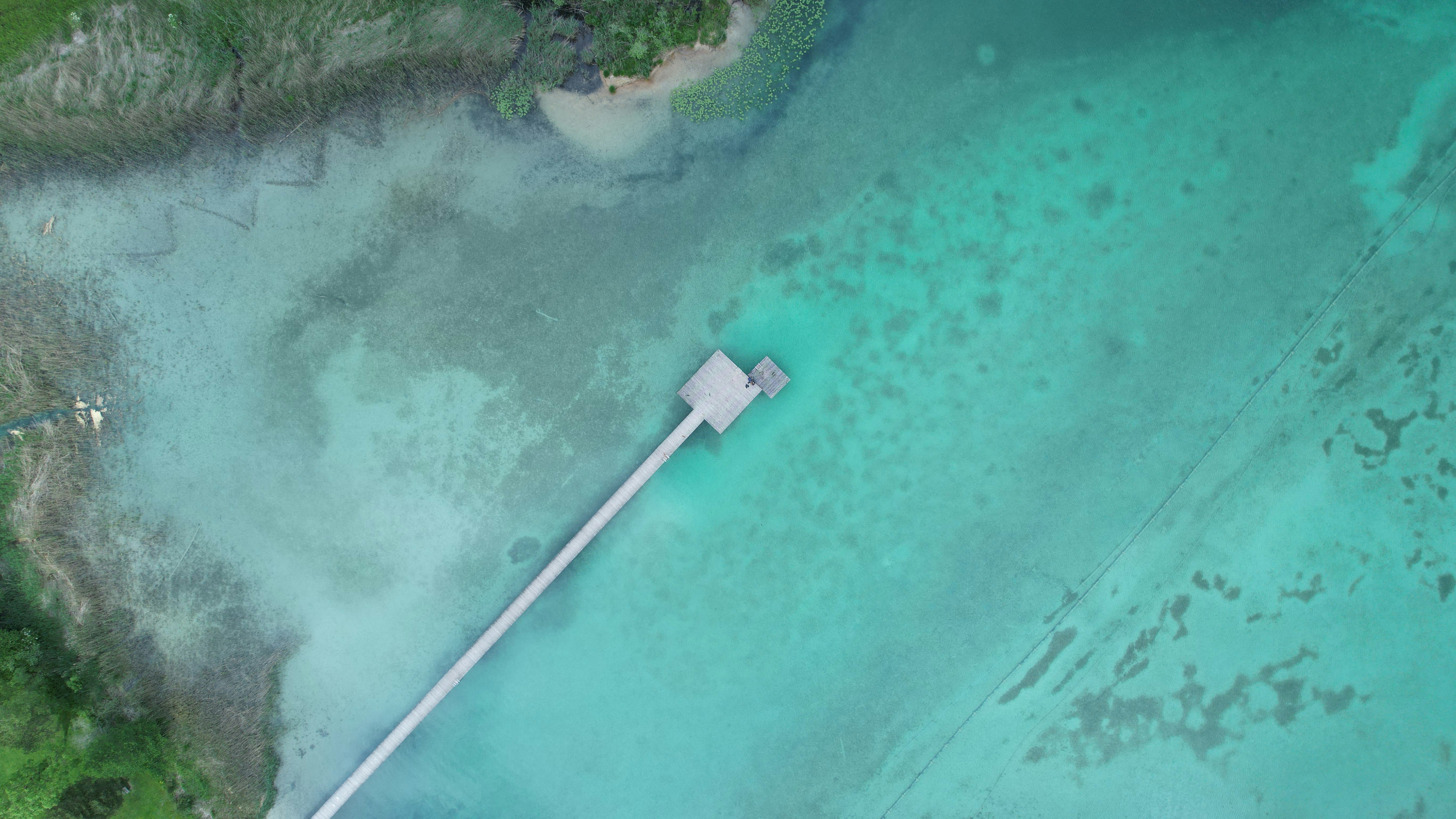 Aerial view of a long pier extending into clear turquoise waters, surrounded by lush greenery and sandy shores.